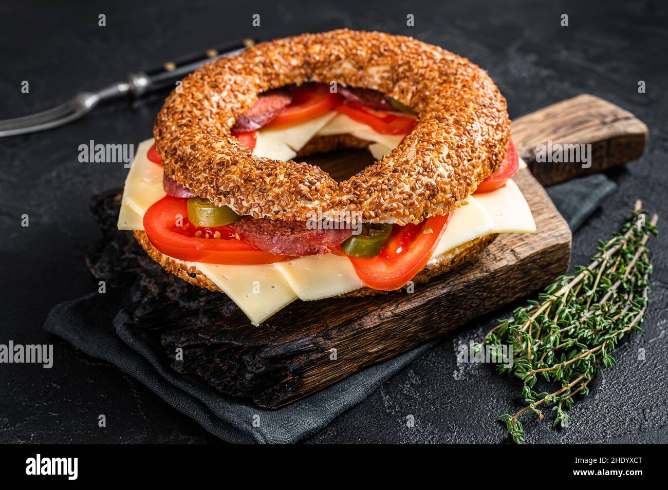 Simit bagel sandwich with lettuce, tomato, yellow cheese and ham. Black ...