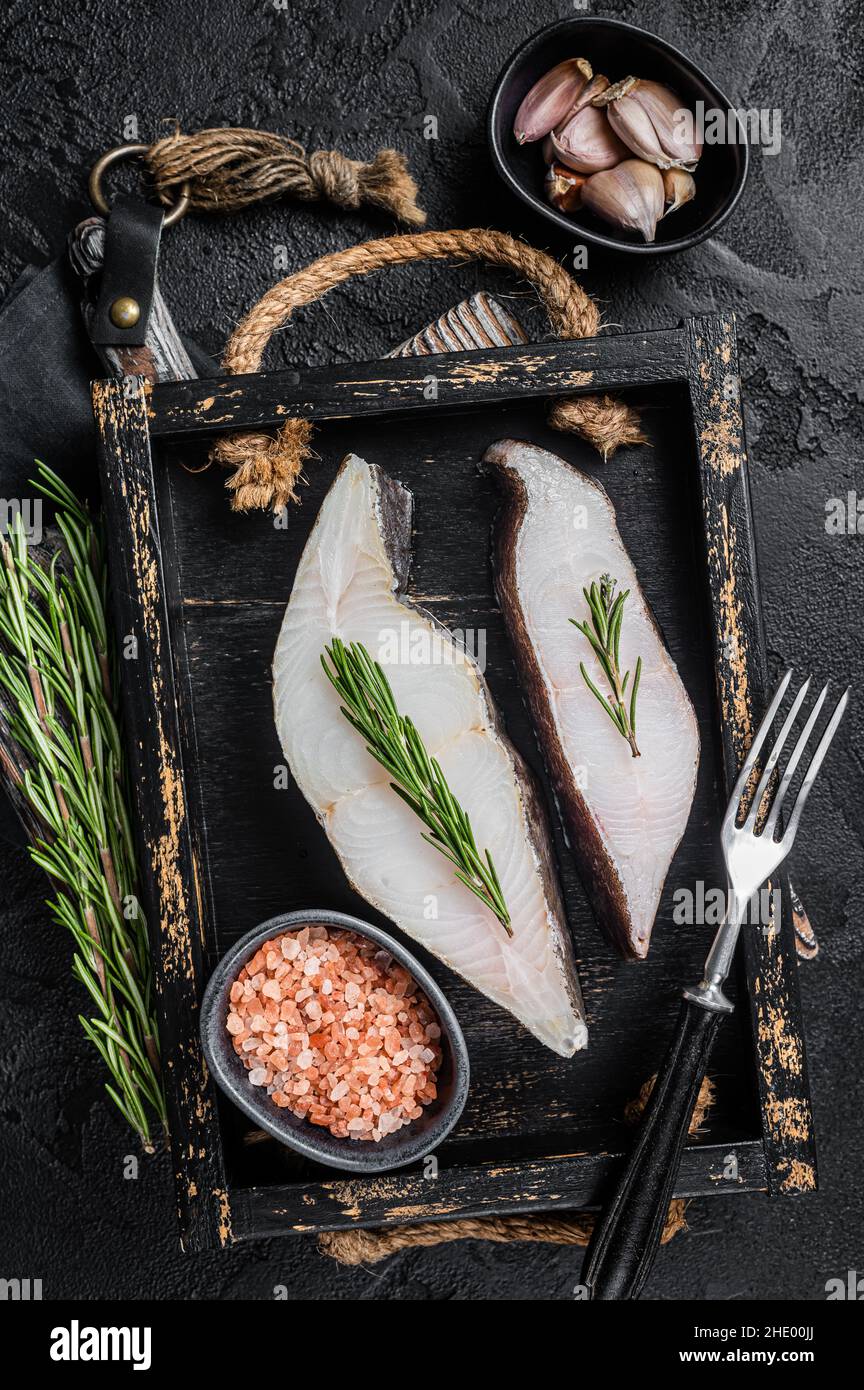 Raw halibut fish steak in wooden tray with herbs. Black background. Top ...