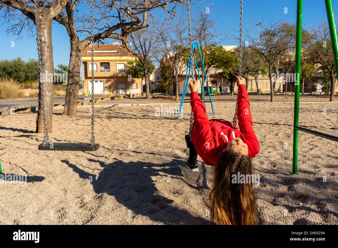 Fearless Hispanic teen lying back while swinging on a swing in a gravel ...