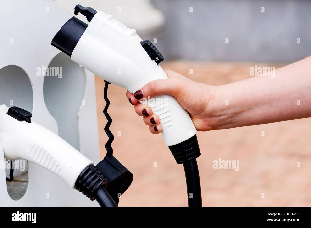 The female hand takes an electric vehicle charging cable. The driver ...