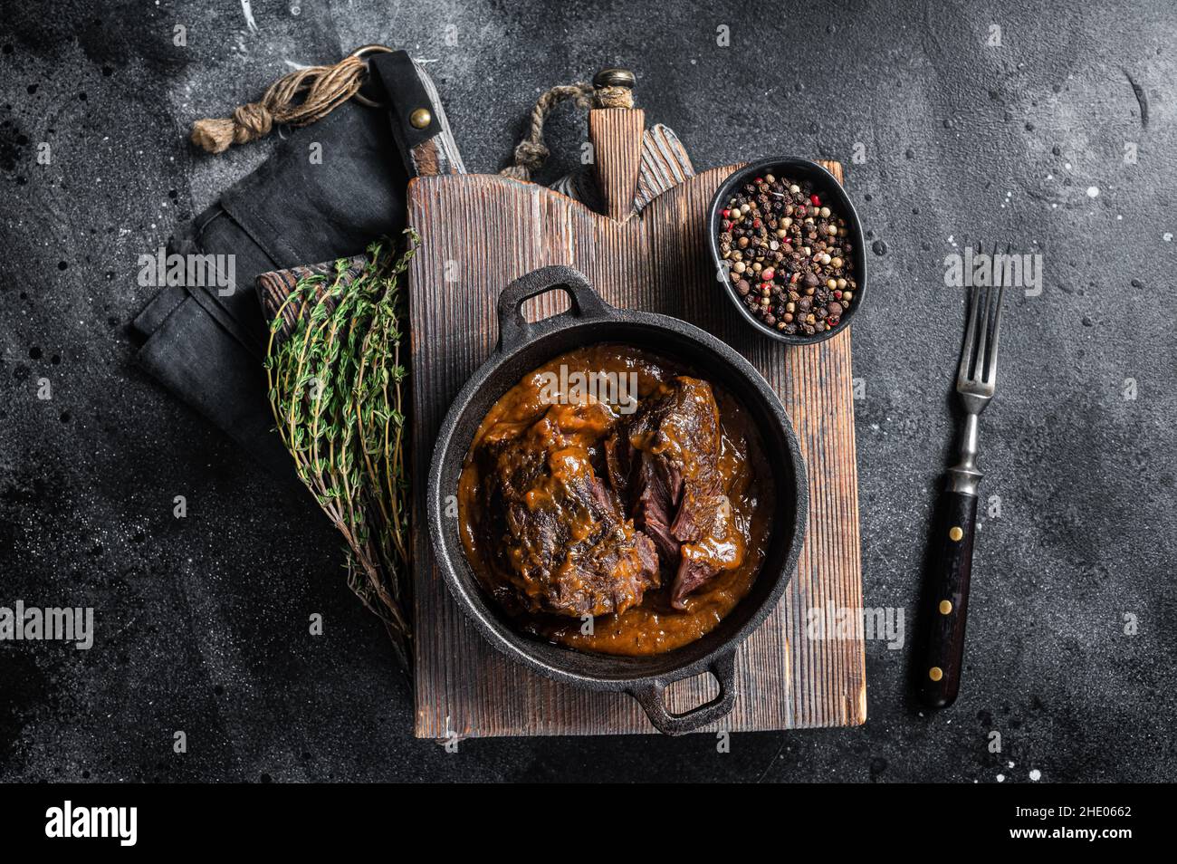 Stewed beef cheeks with brown red wine sauce in skillet. Black ...