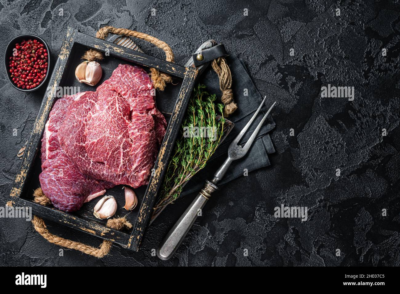 Raw beef cheeks in wooden tray with herbs. Black background. Top view ...