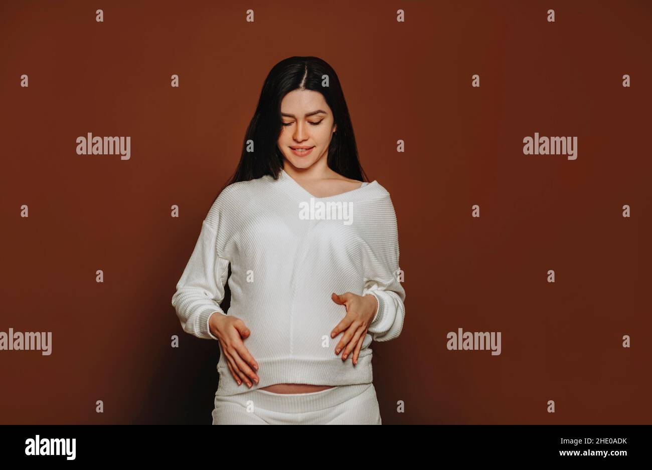 Young happy pregnant woman with long brown hair touching belly, talking ...