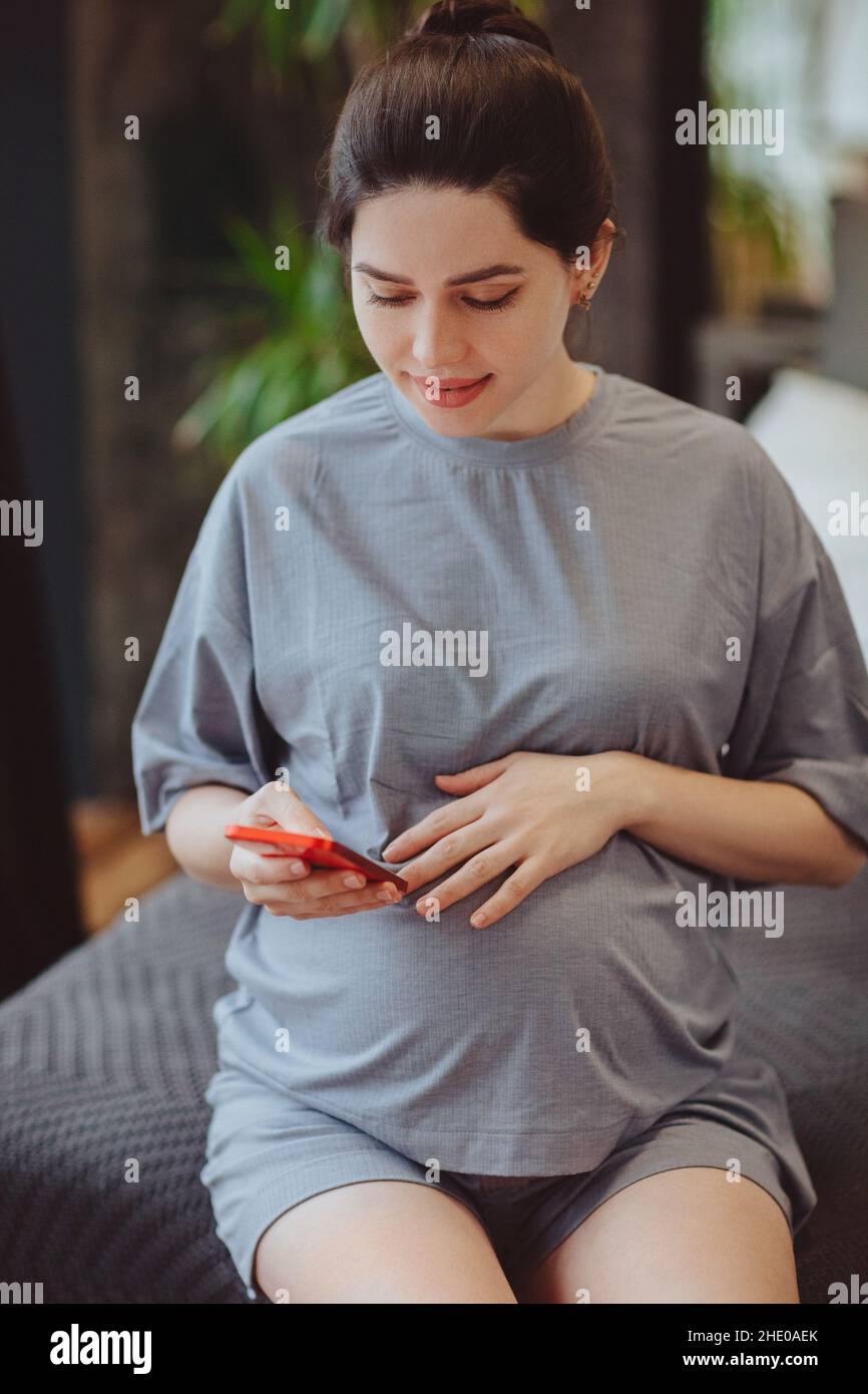 Young smiling pregnant woman touching belly talking on mobile phone ...
