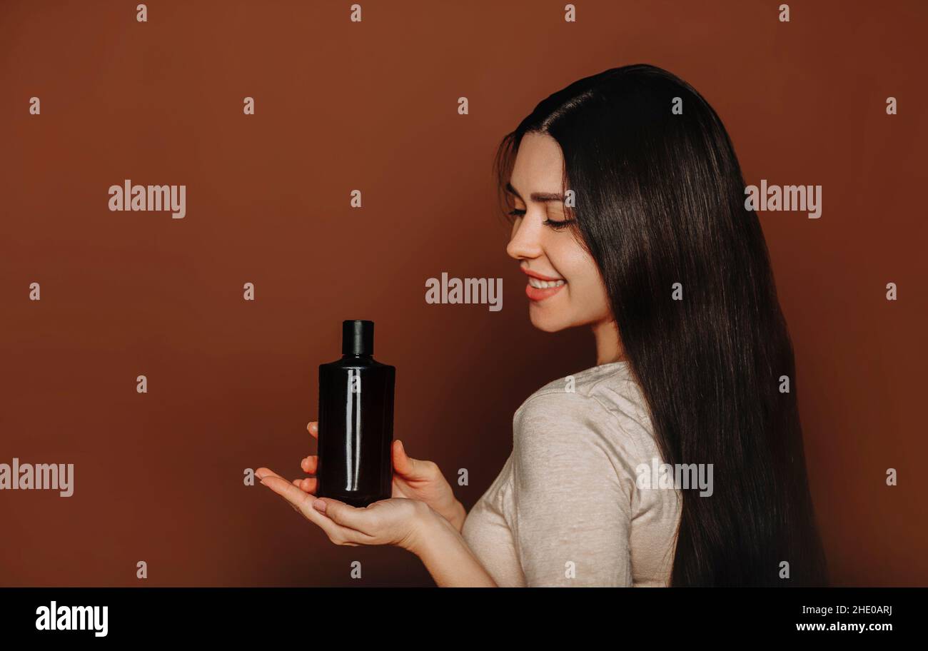 Young smiling woman with long healthy brown hair holding shampoo on ...