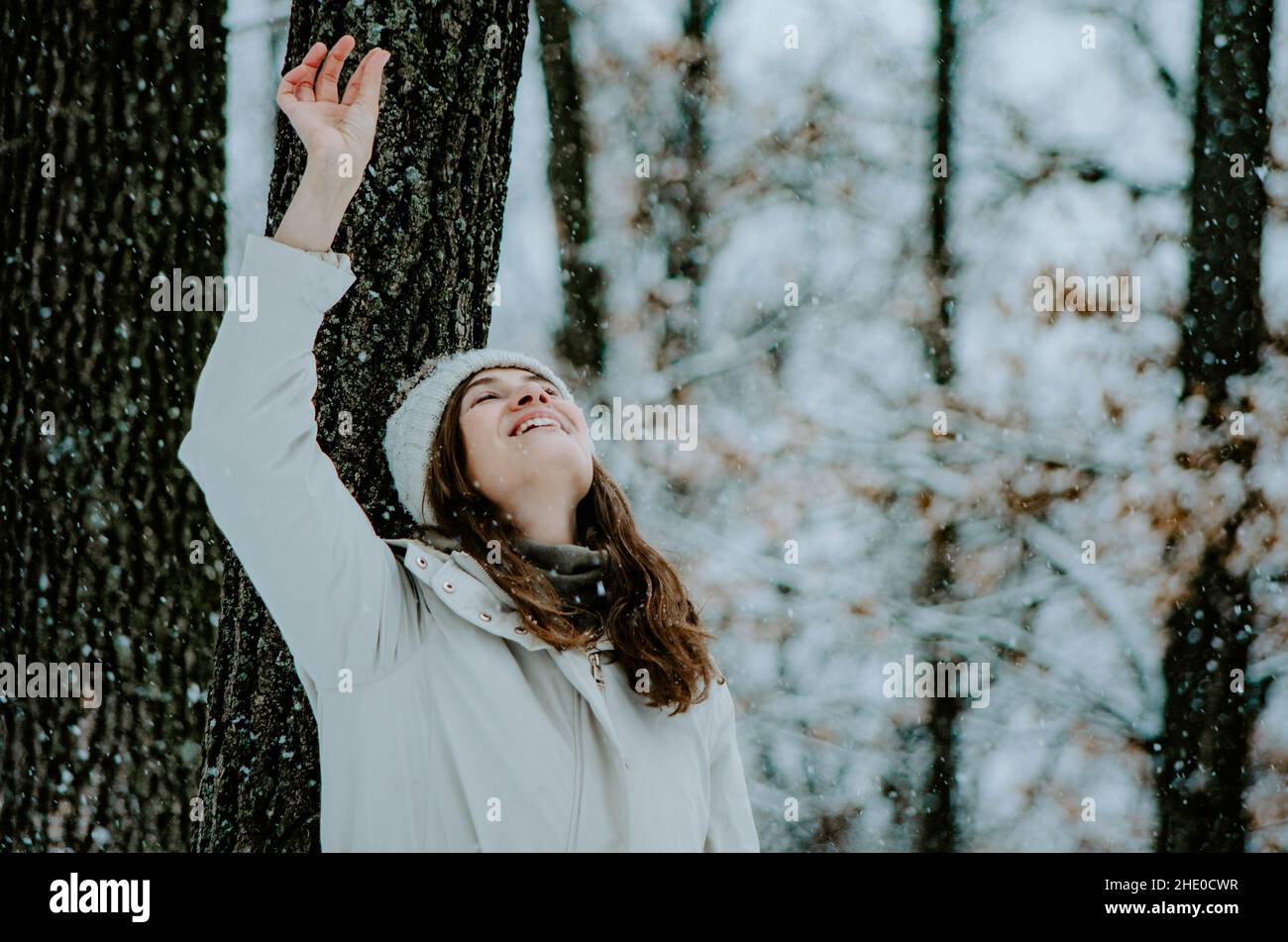 Portrait of a woman enjoying gentle snowfall in winter forest ...
