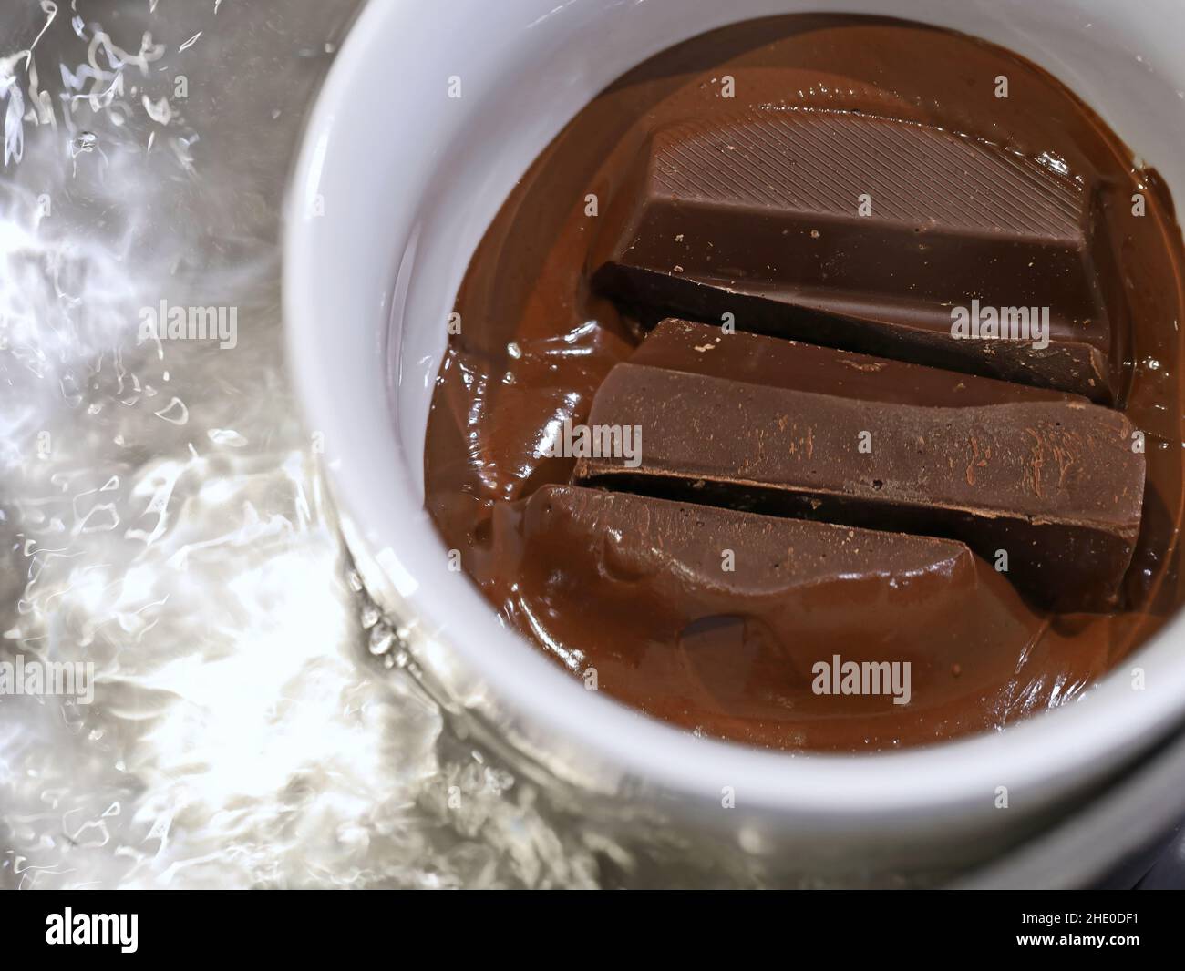 melting dark chocolate in white cup in boiling water pot, close up ...