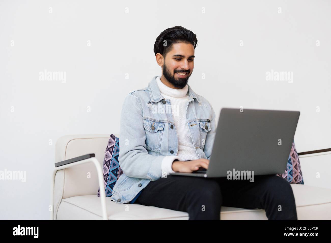 casual indian male using computer on sofa Stock Photo - Alamy
