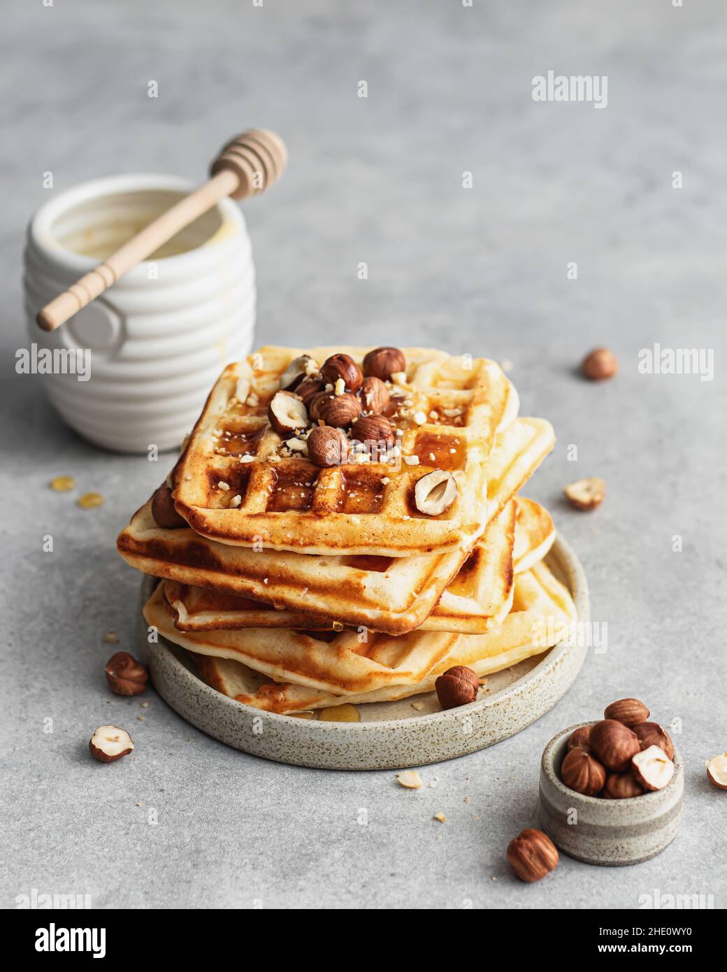 Delicious stack of waffles with hazelnuts and honey on gray background ...