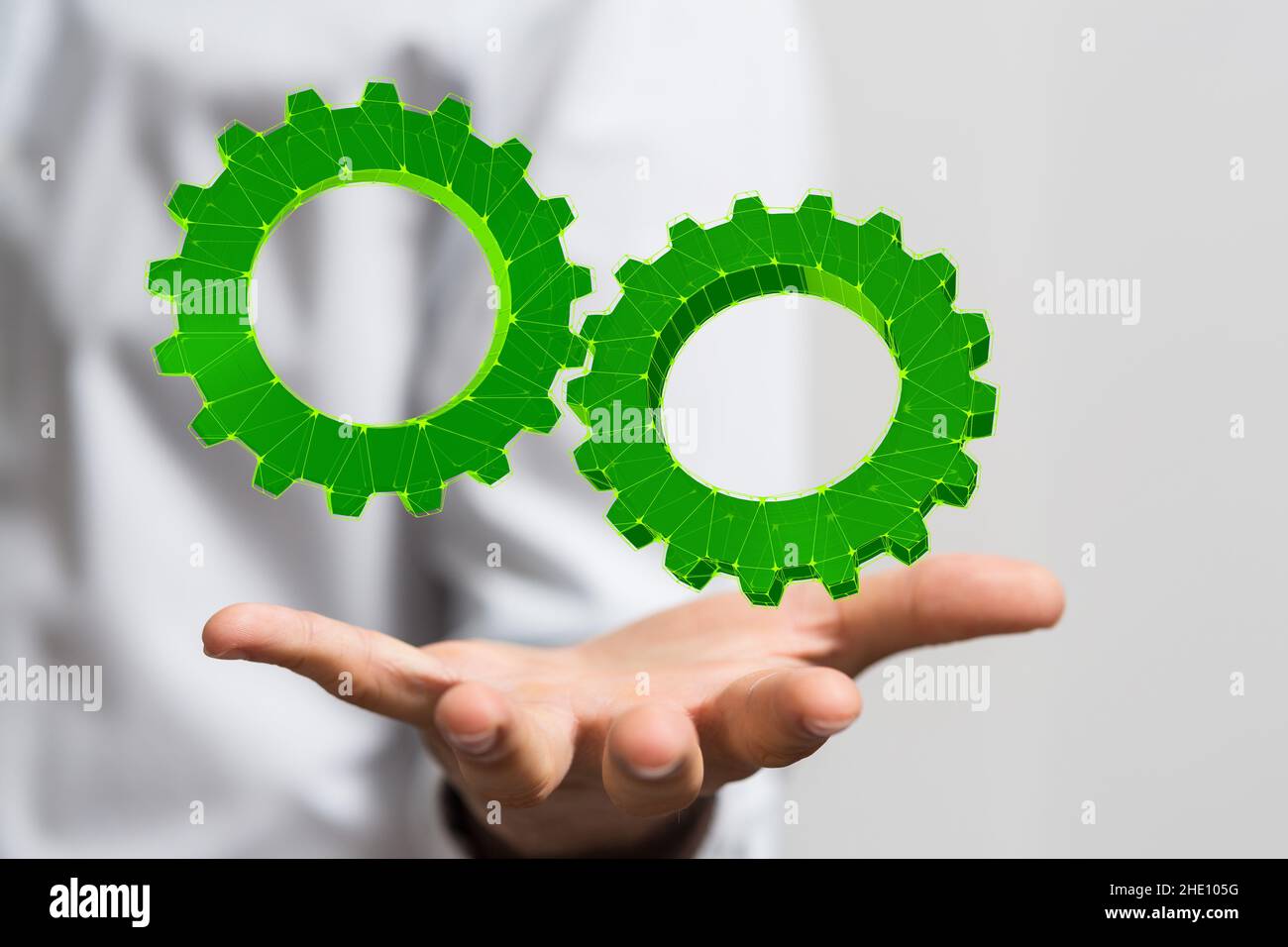 Male's hand holding an illustration of green metallic gears and cogs ...