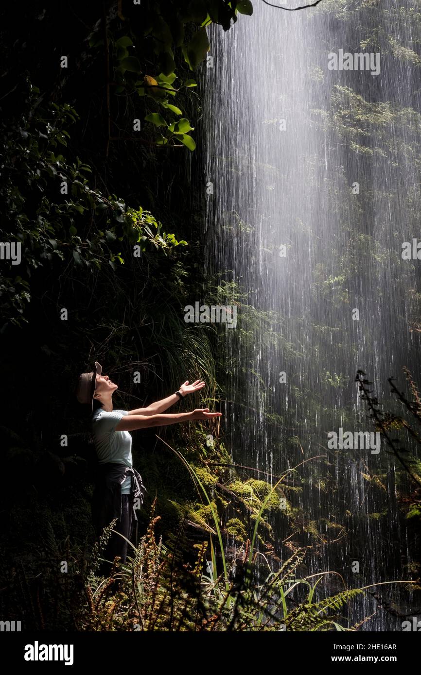 female hiker in a hat extending hands under cold waterfall spray Stock ...