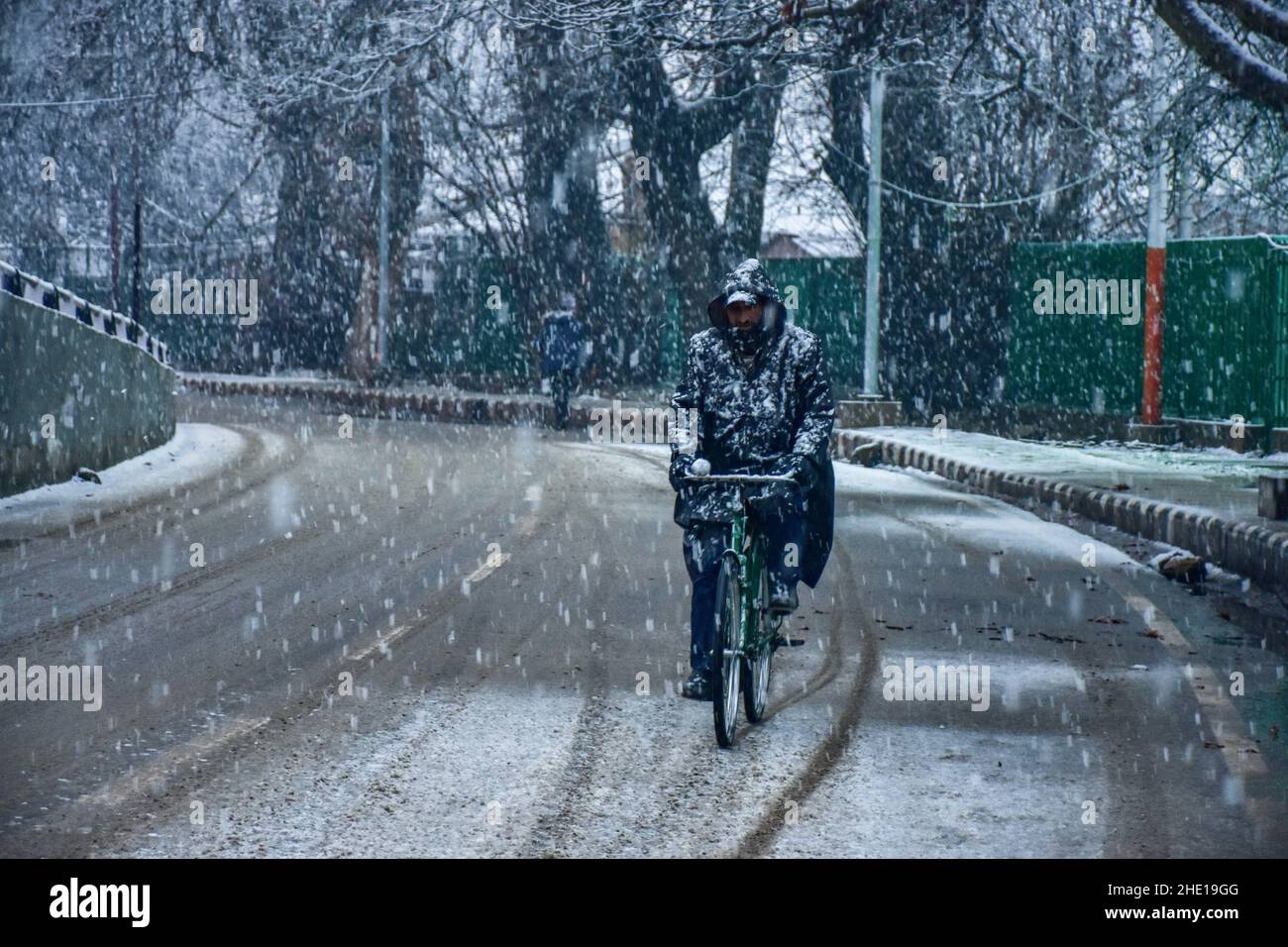 A cyclist rides along a snow covered road during a snowfall in Srinagar ...
