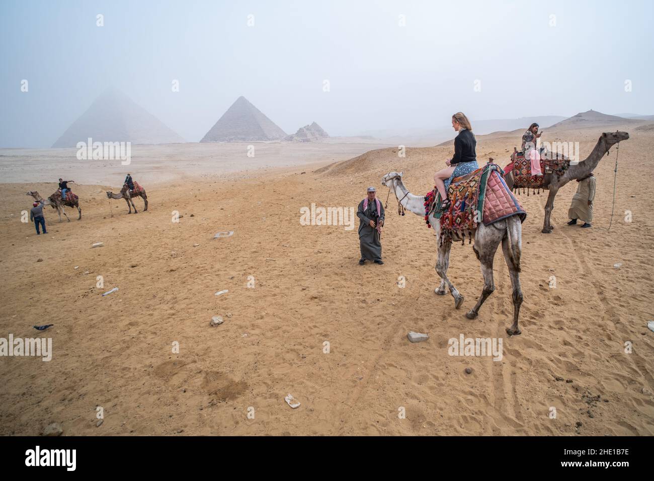 A solo female traveler on a camel ride in the desert with the pyramids ...
