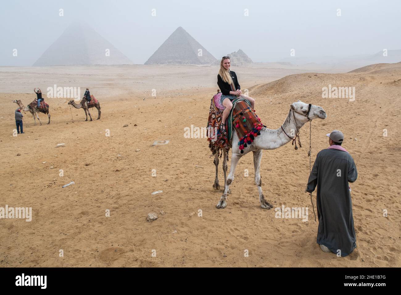 A solo female traveler on a camel ride in the desert with the pyramids ...