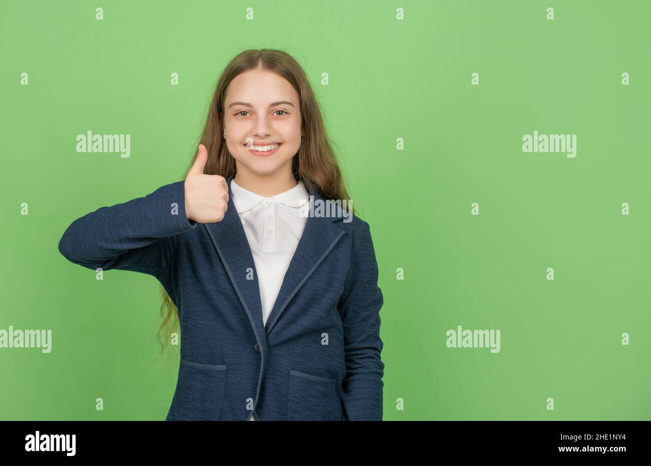 happy kid in school uniform showing thumb up on green background with ...