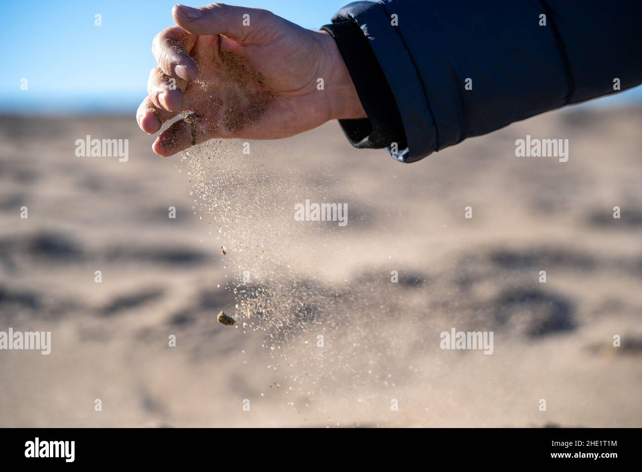 Selective focus of a man's hand dropping sand through his fingers in a ...