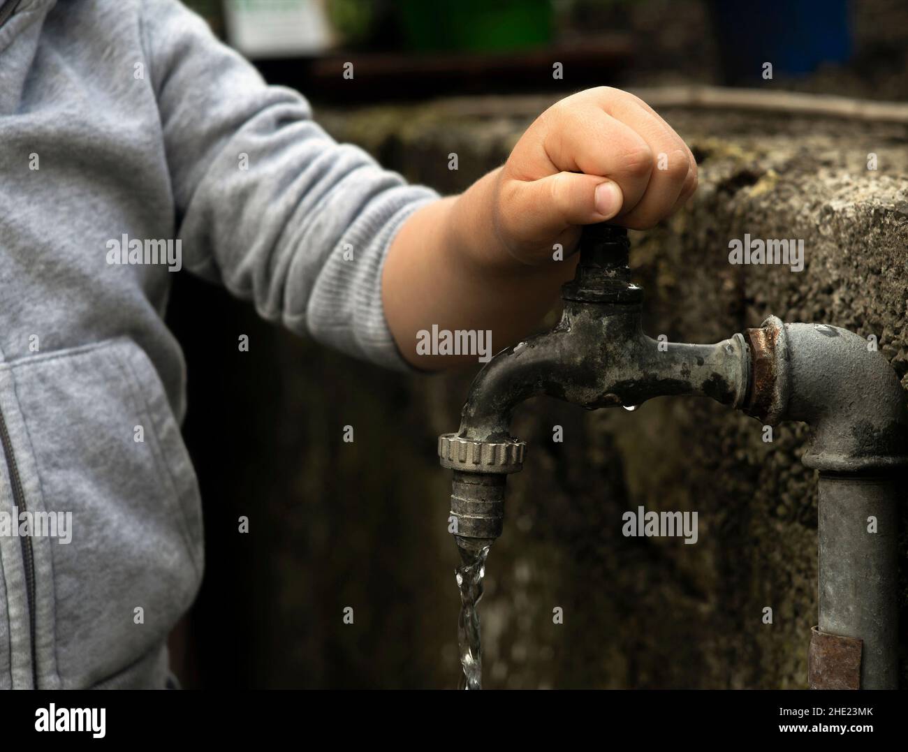 Hand from a child is turning tap water valve and letting water out ...