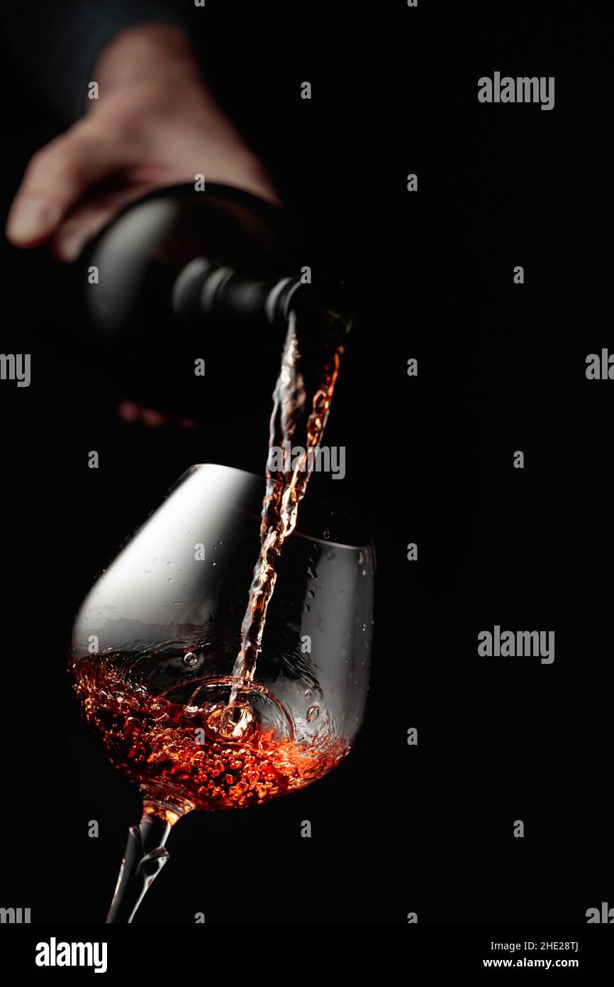 Pouring brandy in a glass goblet. Black background with copy space ...
