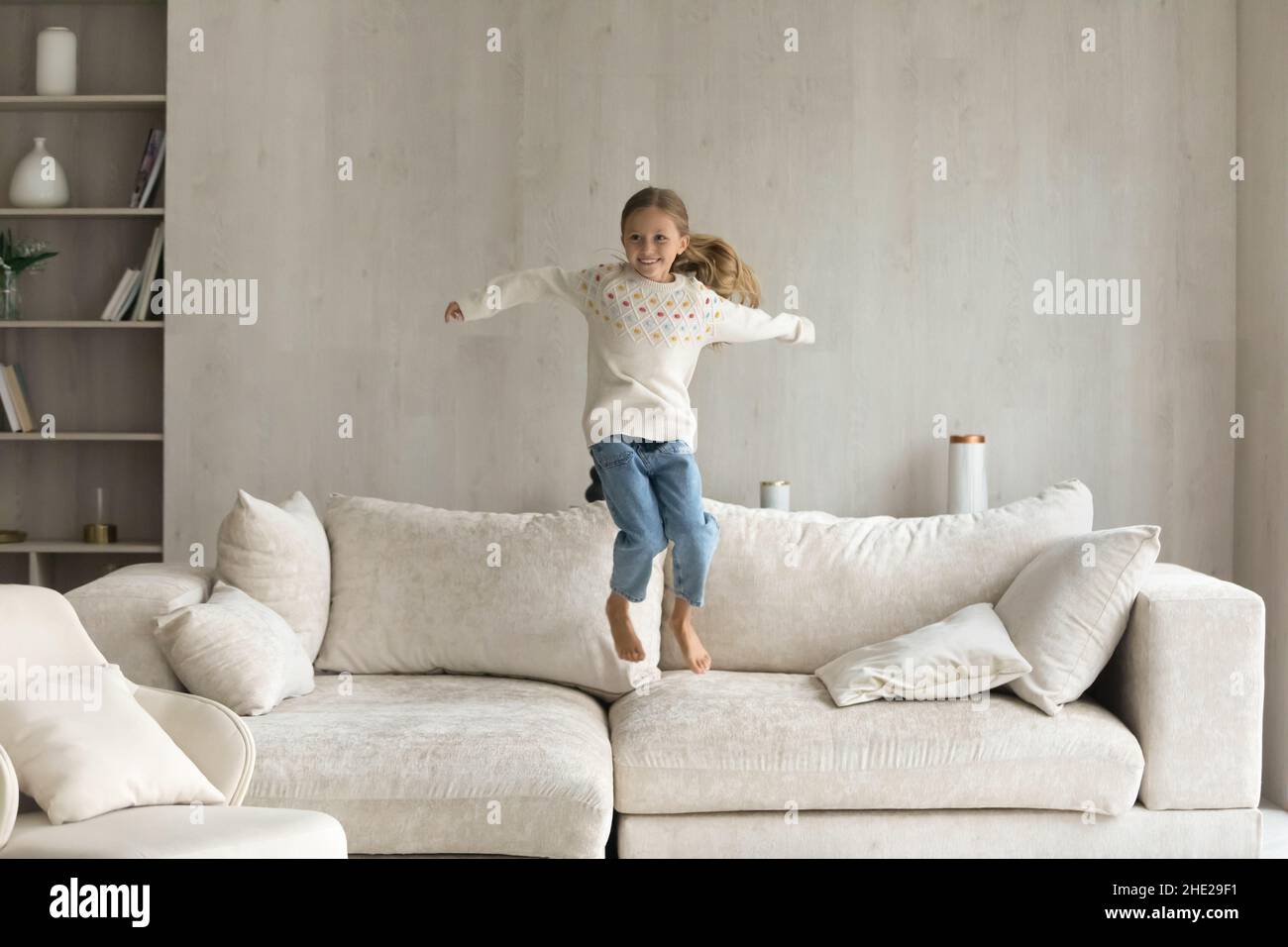 Excited cheerful small 7s kid girl jumping on sofa Stock Photo - Alamy