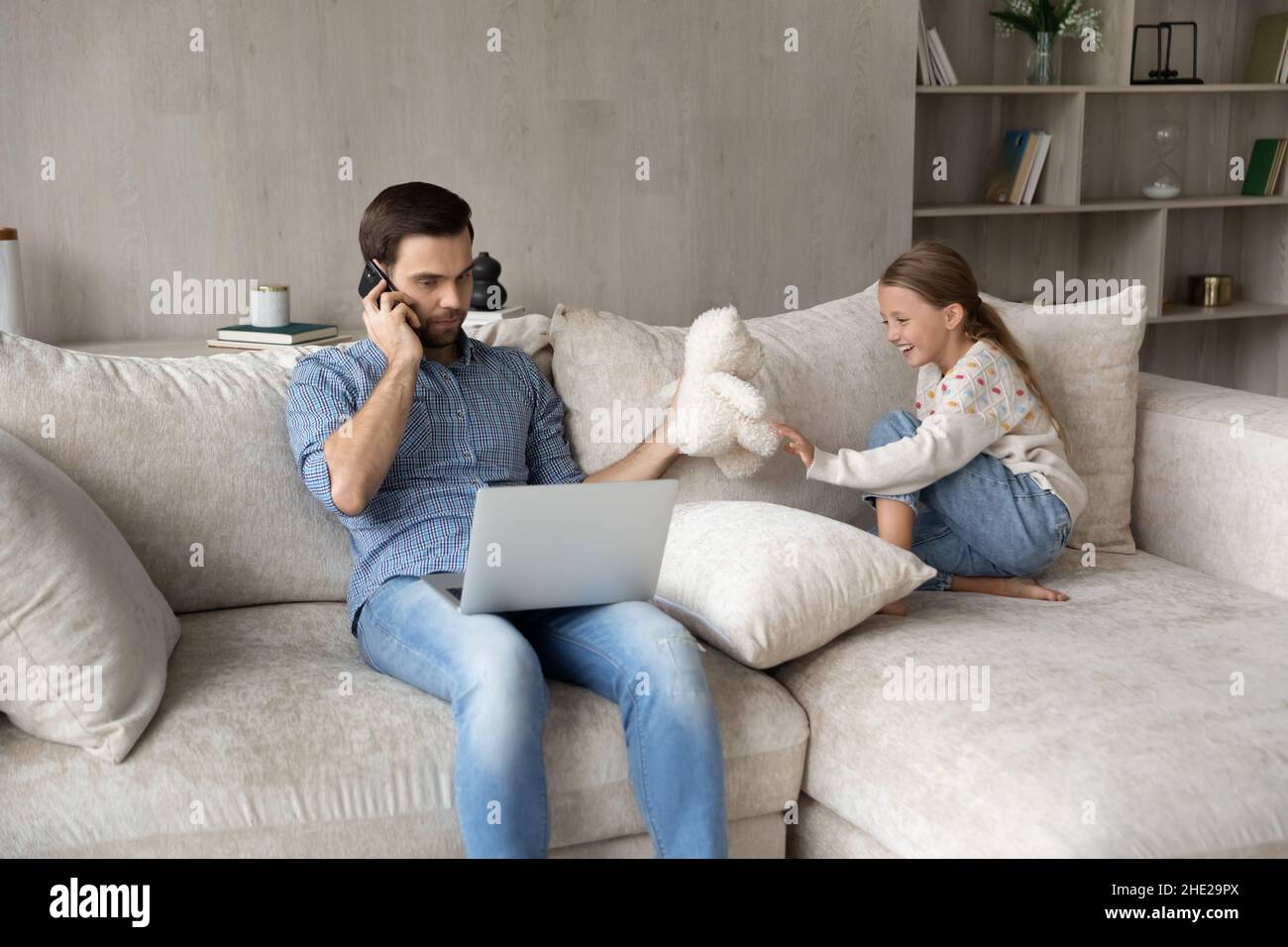Focused young father multitasking, working and playing with kid Stock ...
