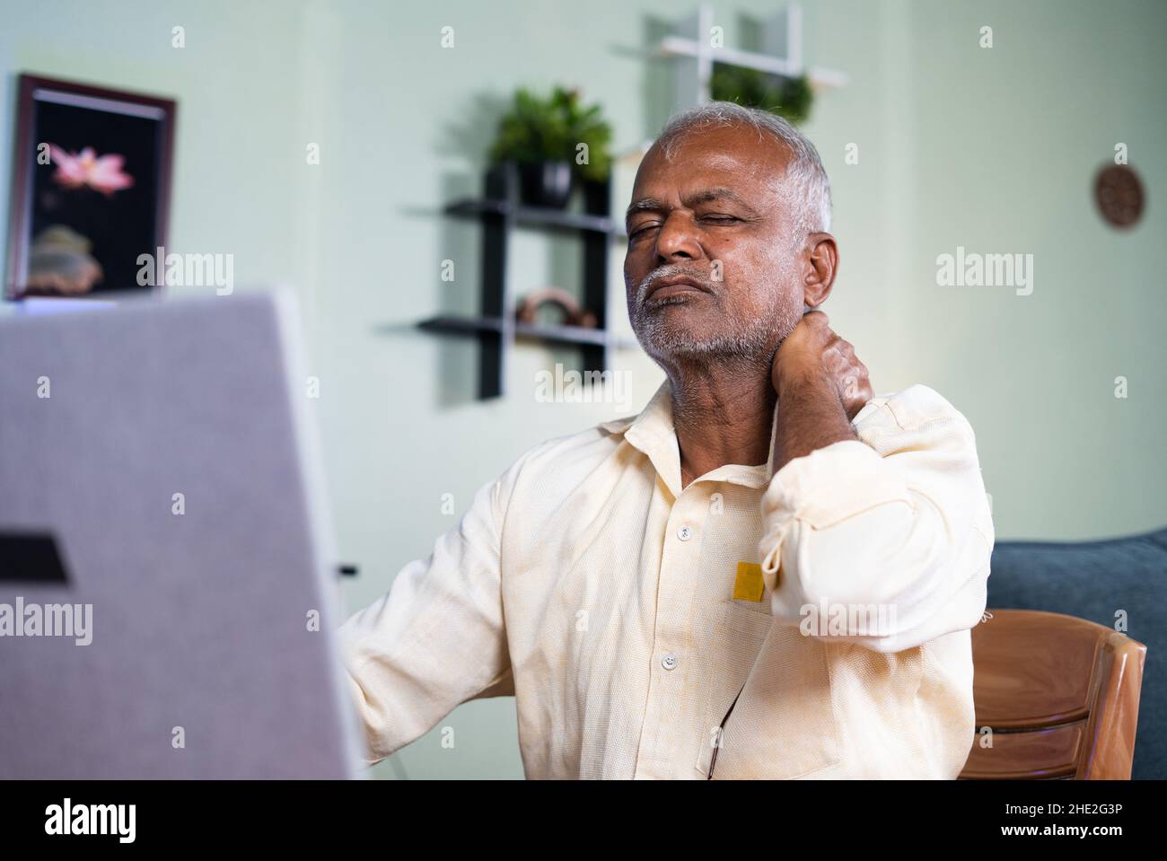 Indian senior old man suffering from neck pain while working on laptop ...