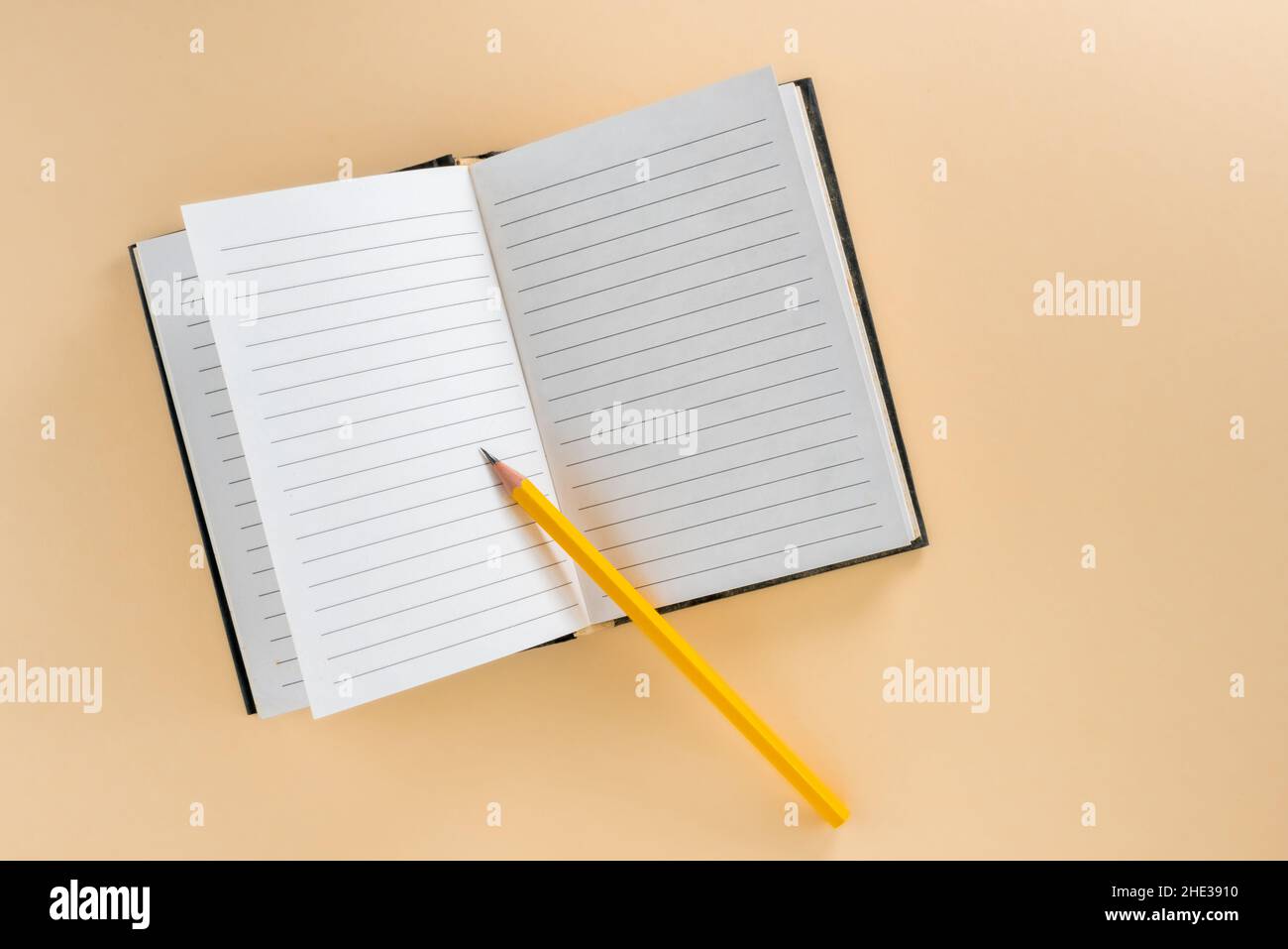 Open lined notebook with yellow pencil isolated on light brown ...