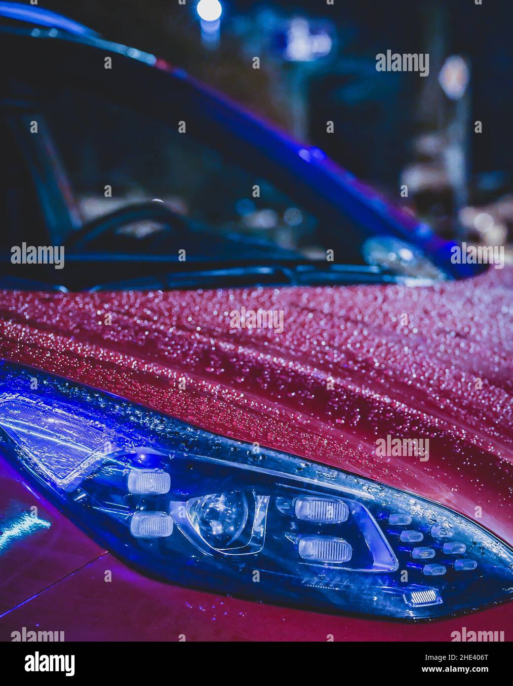 Rain drops on red car. Neon street lights reflecting on the car's ...