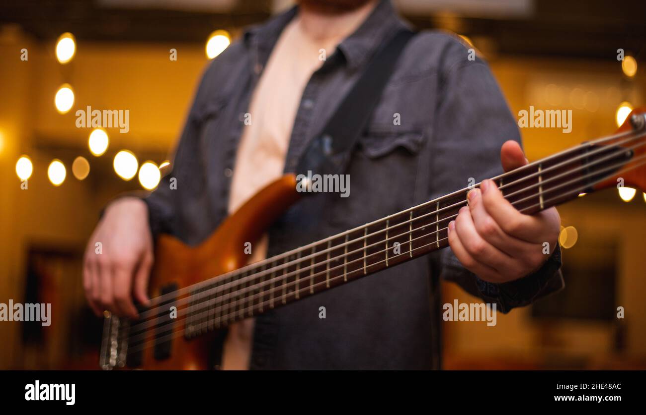 A young guy with a beard plays a bass guitar with five strings Stock Photo - Alamy