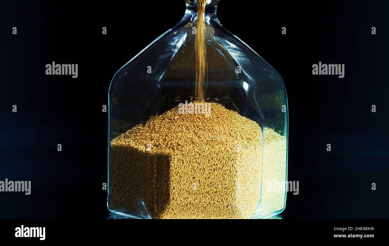 Golden sand inside transparent hourglass isolated on black background ...