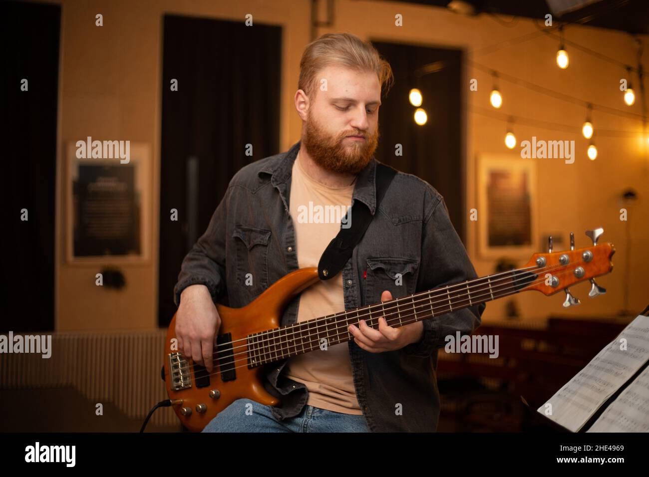 A young guy with a beard plays a bass guitar with five strings Stock ...