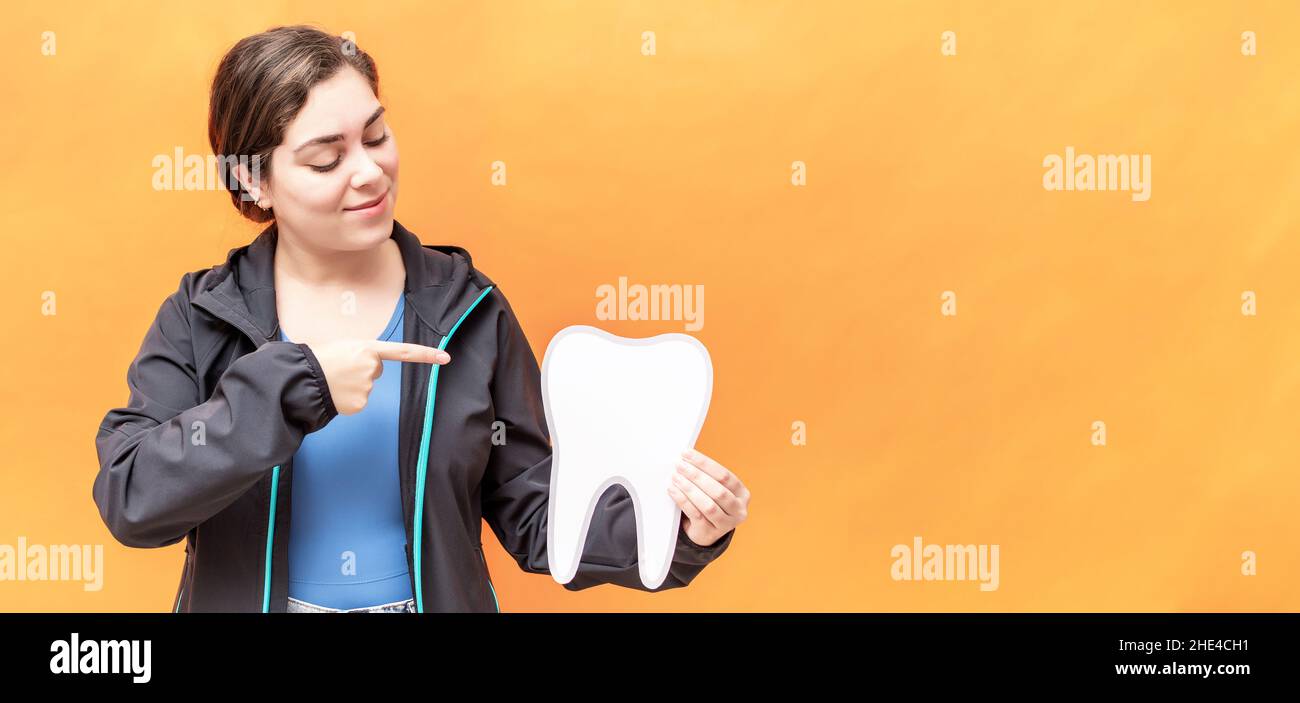 Girl pointing to a tooth shape, isolated over orange background Stock ...