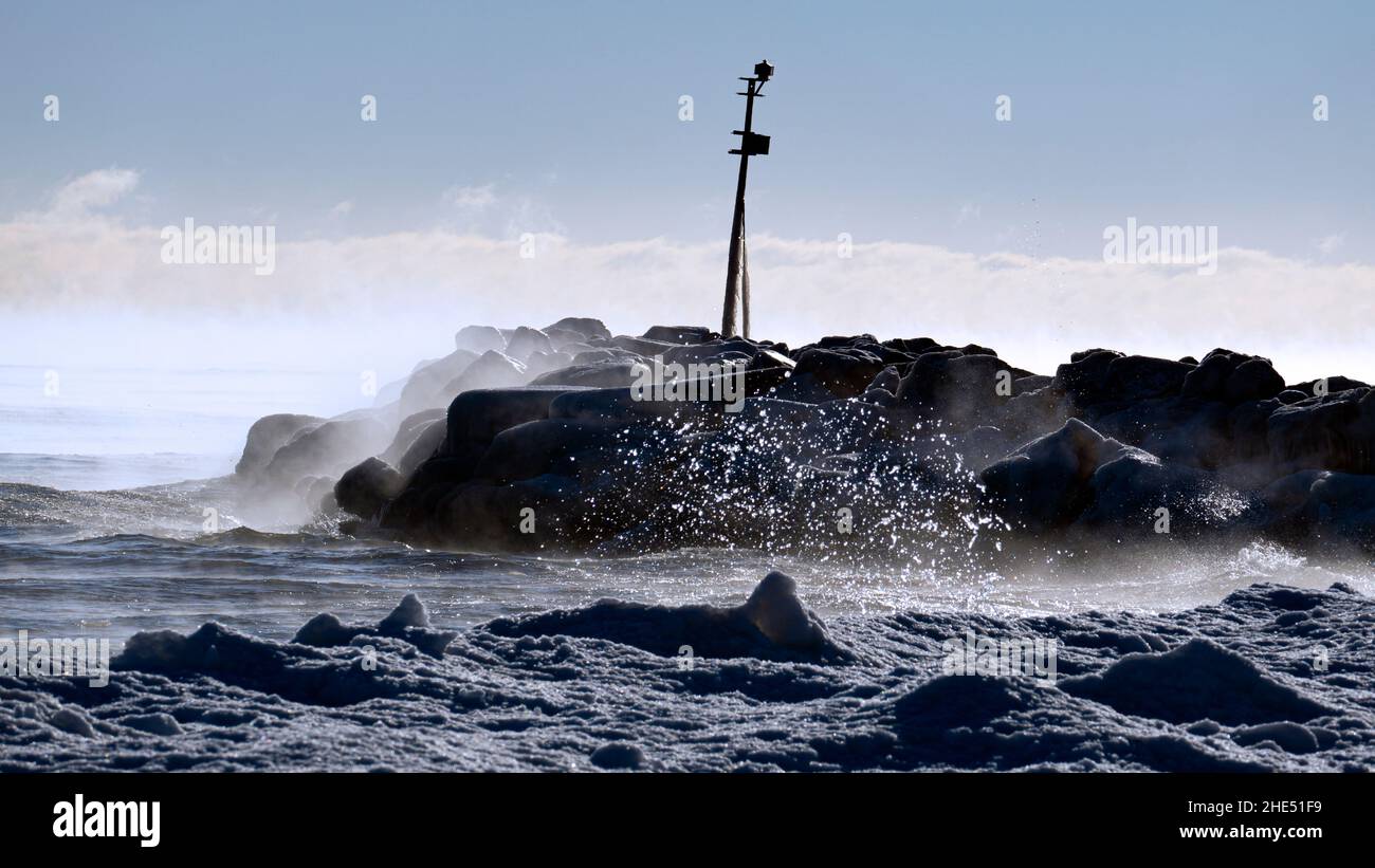 Waves crash against the icy Lake Michigan shoreline with steam coming ...