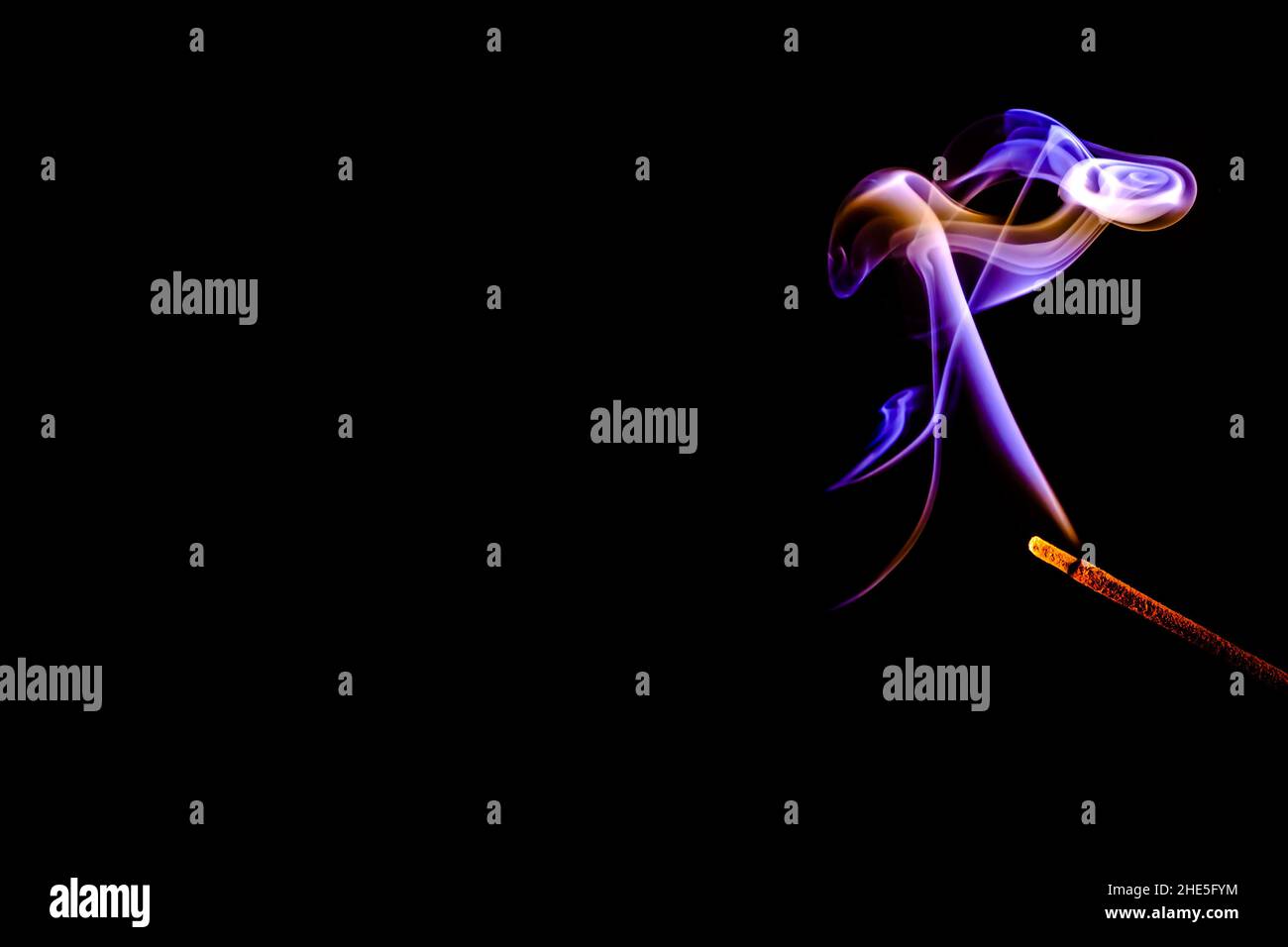 An aroma stick burns and smokes. Colored smoke is filmed in slow motion ...