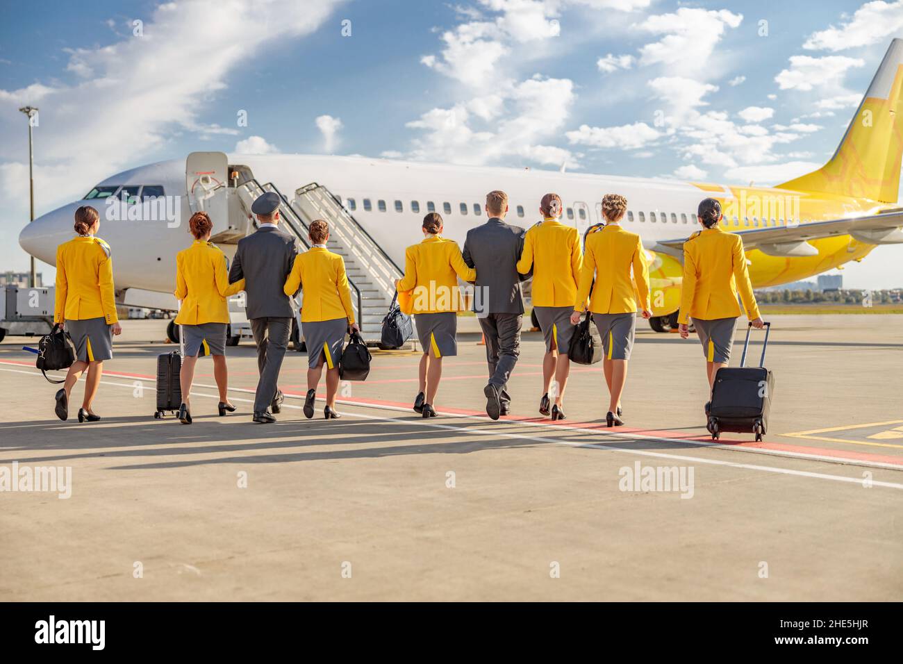 Back view of flight attendants and male pilots in work uniforms heading ...