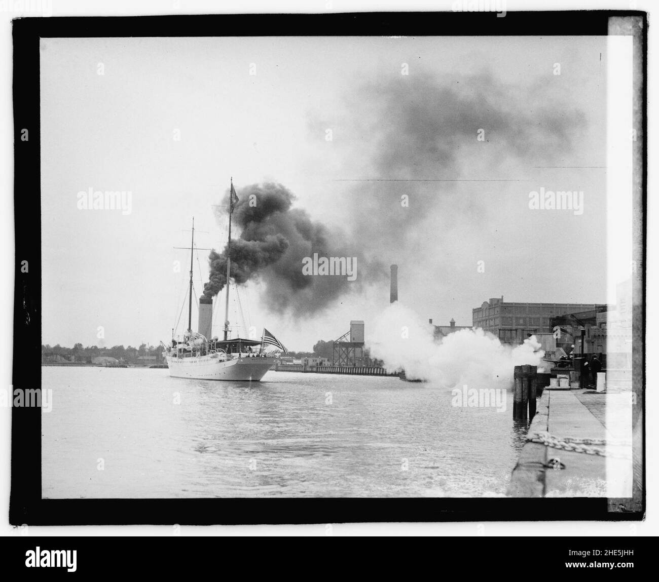 Sailing ship in harbor; smokestack with billowing smoke in background ...