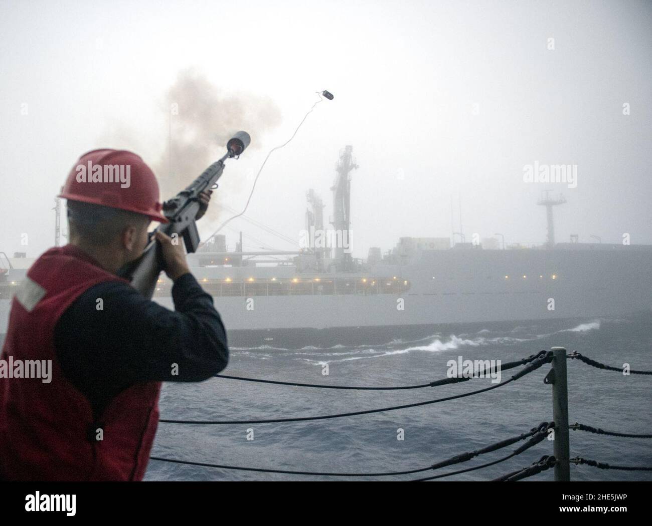 Sailor firing shot line from USS Lake Champlain (CG-57) to USNS Yukon ...