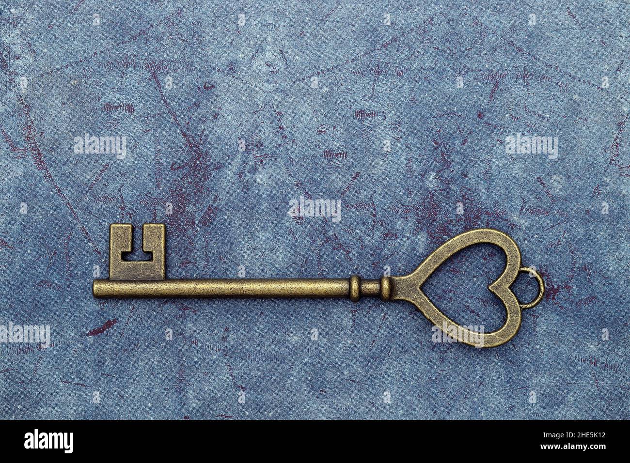 golden heart shaped vintage key on a grungy blue leather background ...