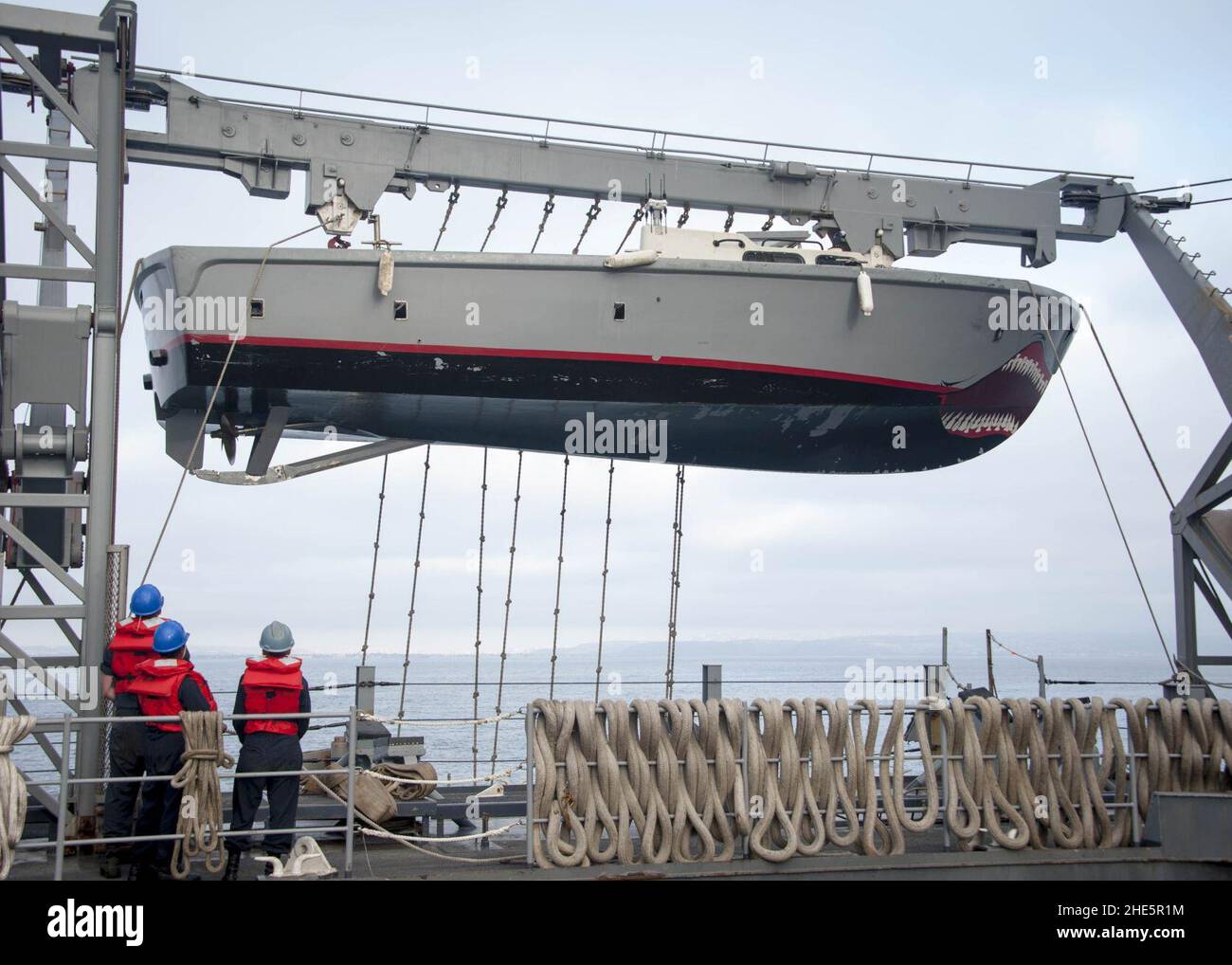 Sailors raise a landing craft personnel large onto the ship's boat deck ...