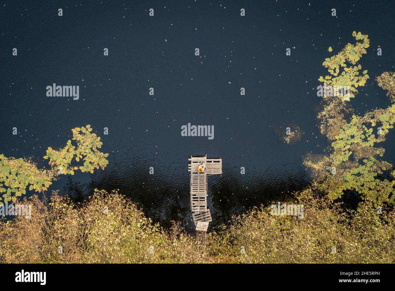 Aerial shot of woman in a yellow jacket relaxing on a wooden pier on a ...