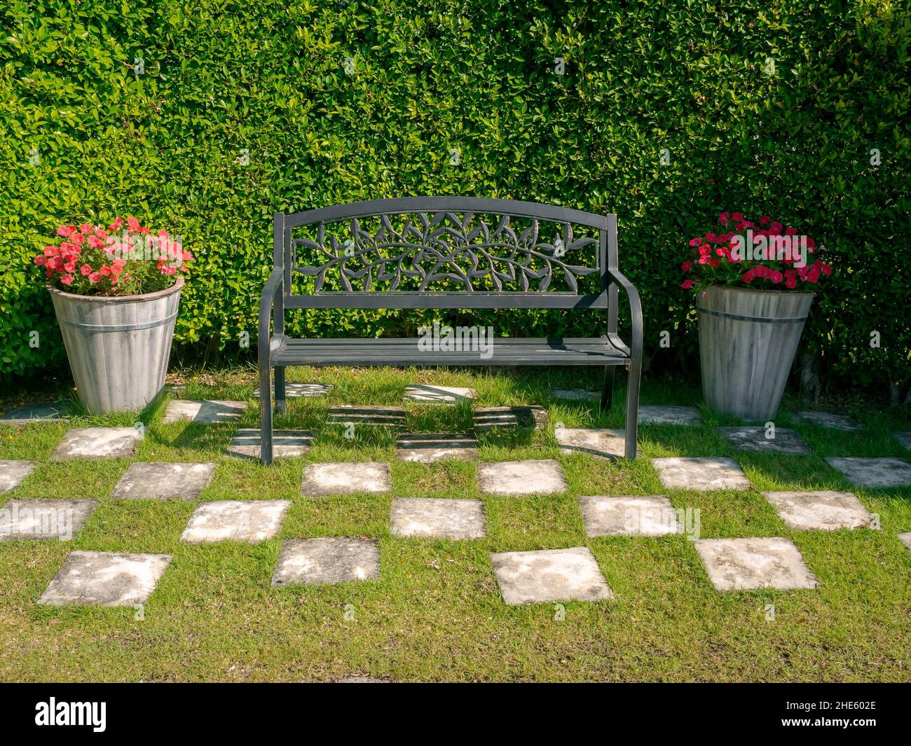 Empty black iron bench decorated between two flower pots on the green ...
