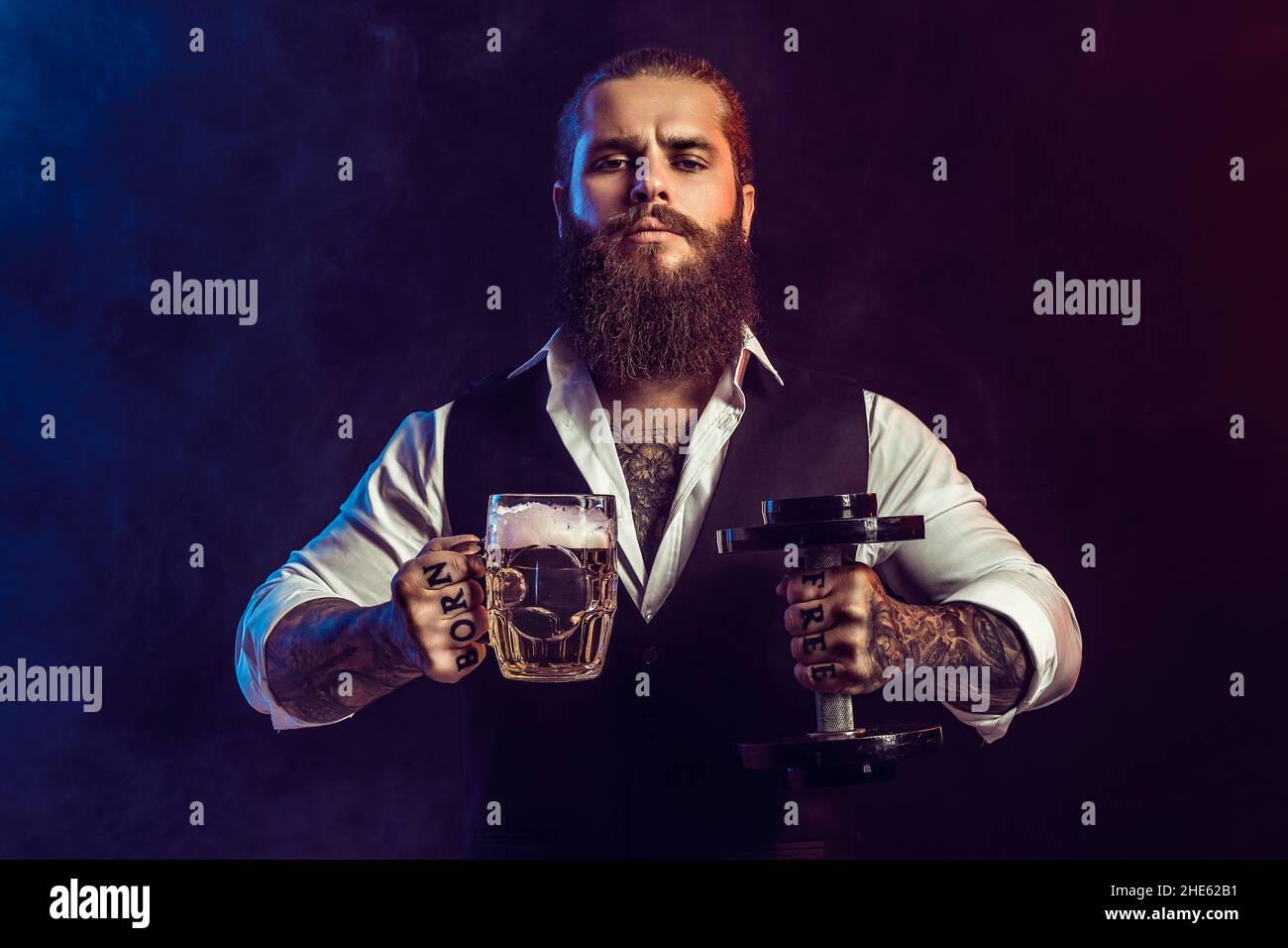 man holds dumbbell and mug of beer on dark background. Concept of ...