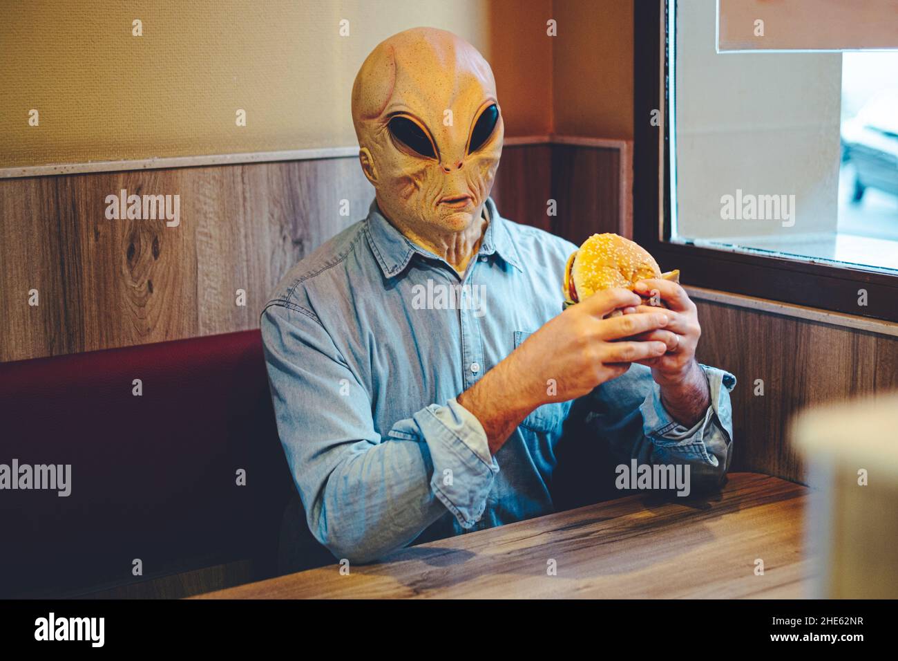Extraterrestrial ufo alien eating an hamburger at the fast food sitting ...