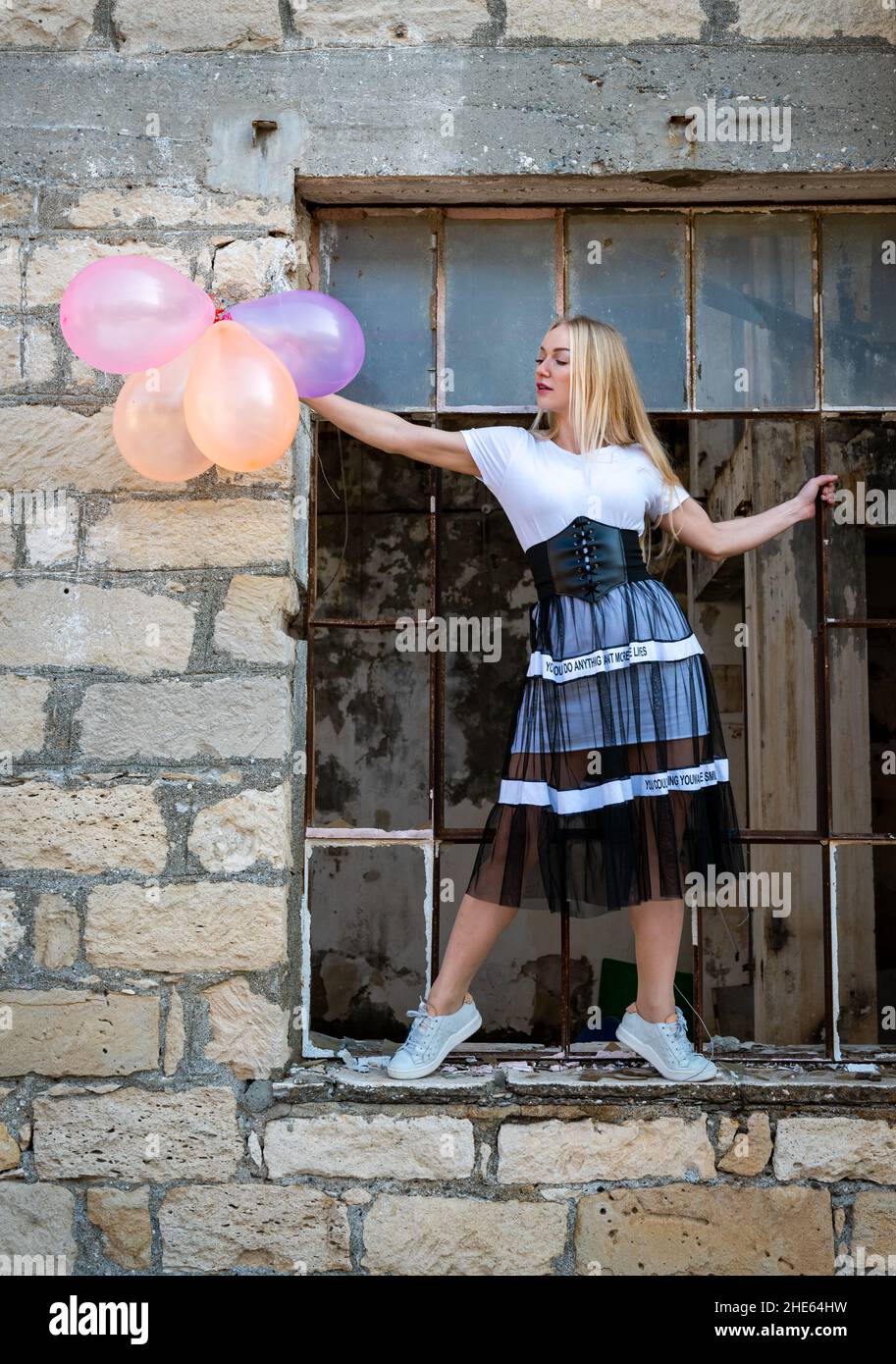 Happy woman having fun holding colorful air balloons on a broken window ...