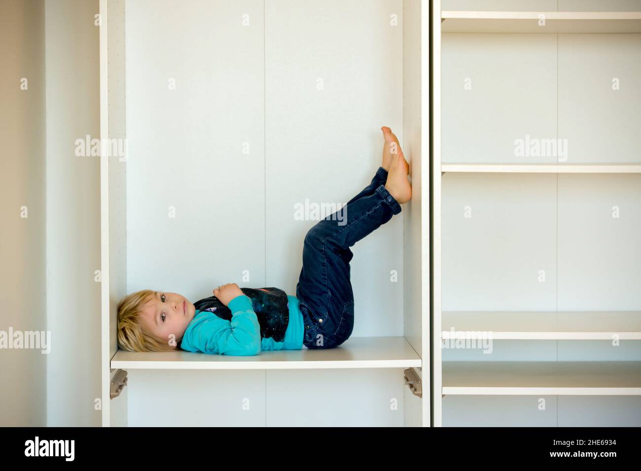 Cute child, sit in a white box in open wardrope, making funny faces ...