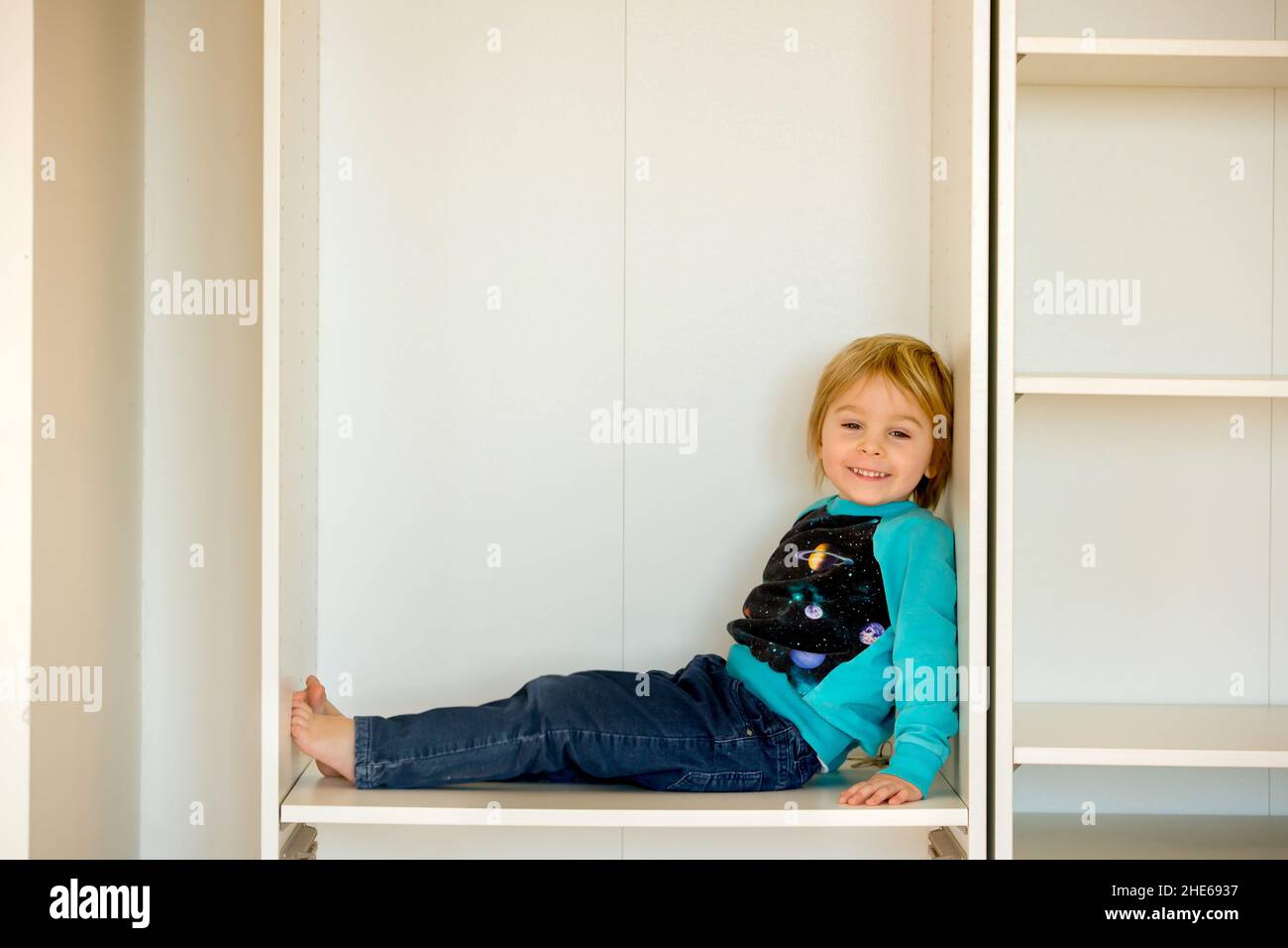 Cute child, sit in a white box in open wardrope, making funny faces ...