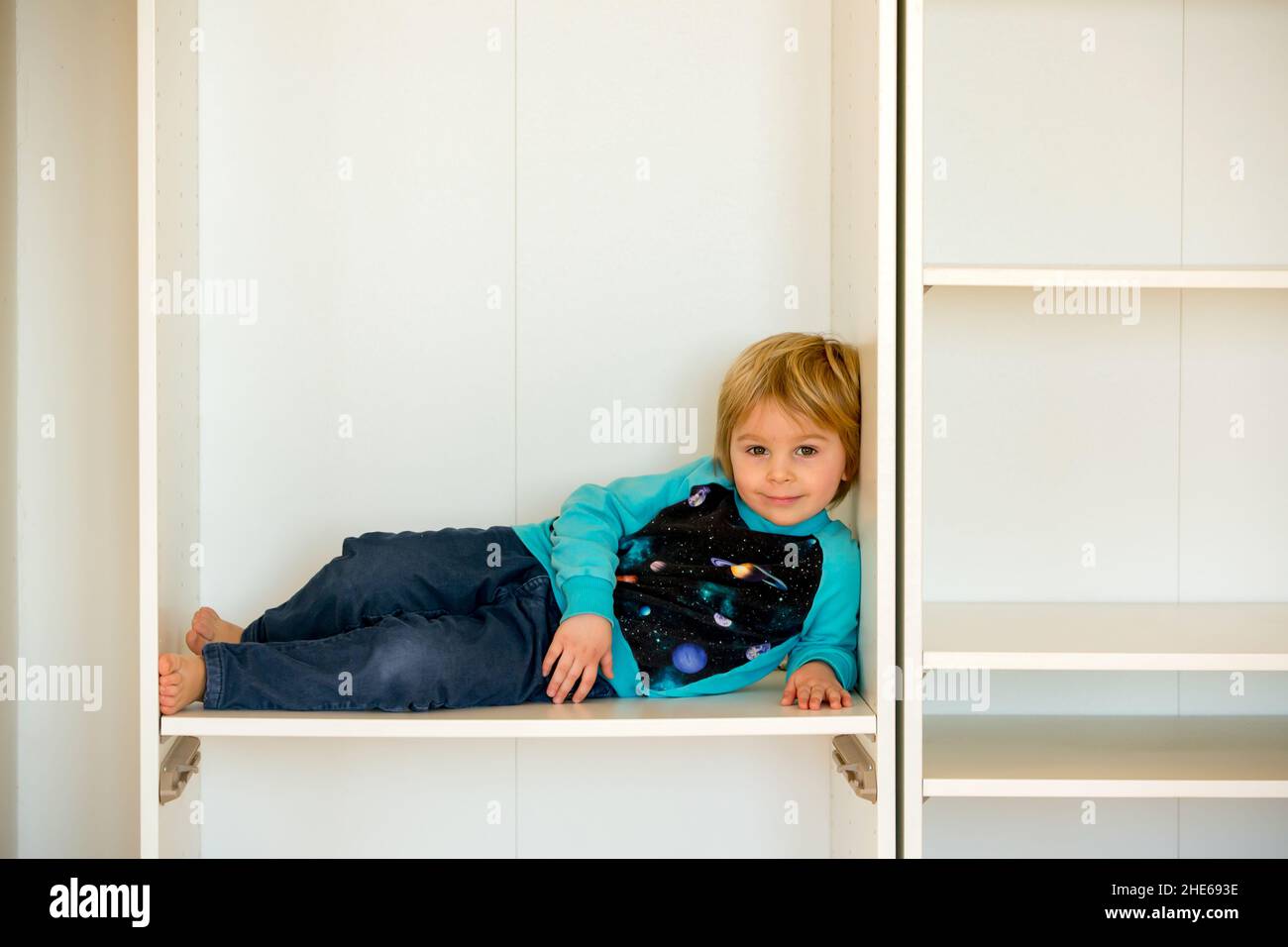Cute child, sit in a white box in open wardrope, making funny faces ...