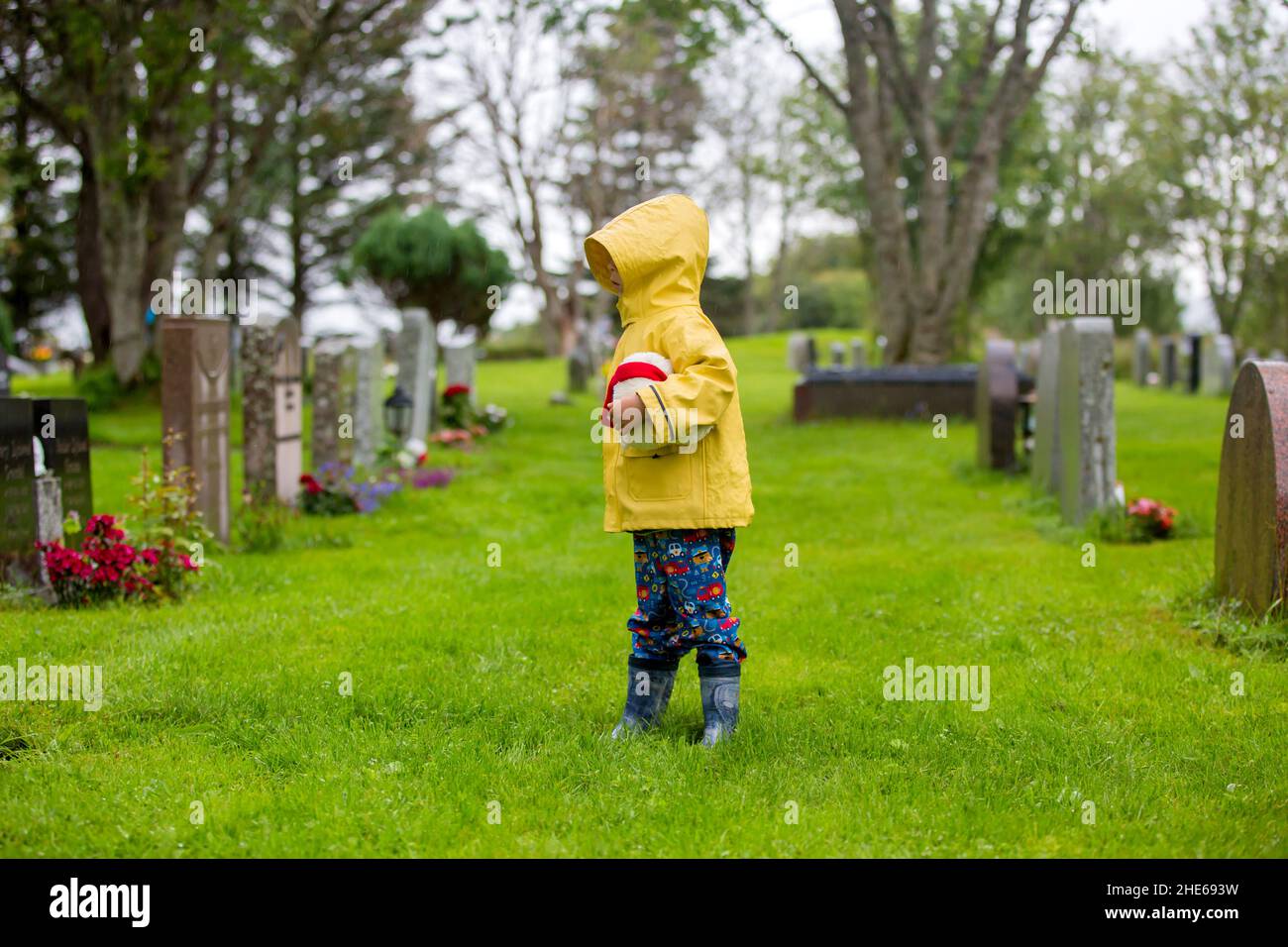 Sad little child, blond boy, standing in the rain on cemetery, sad ...