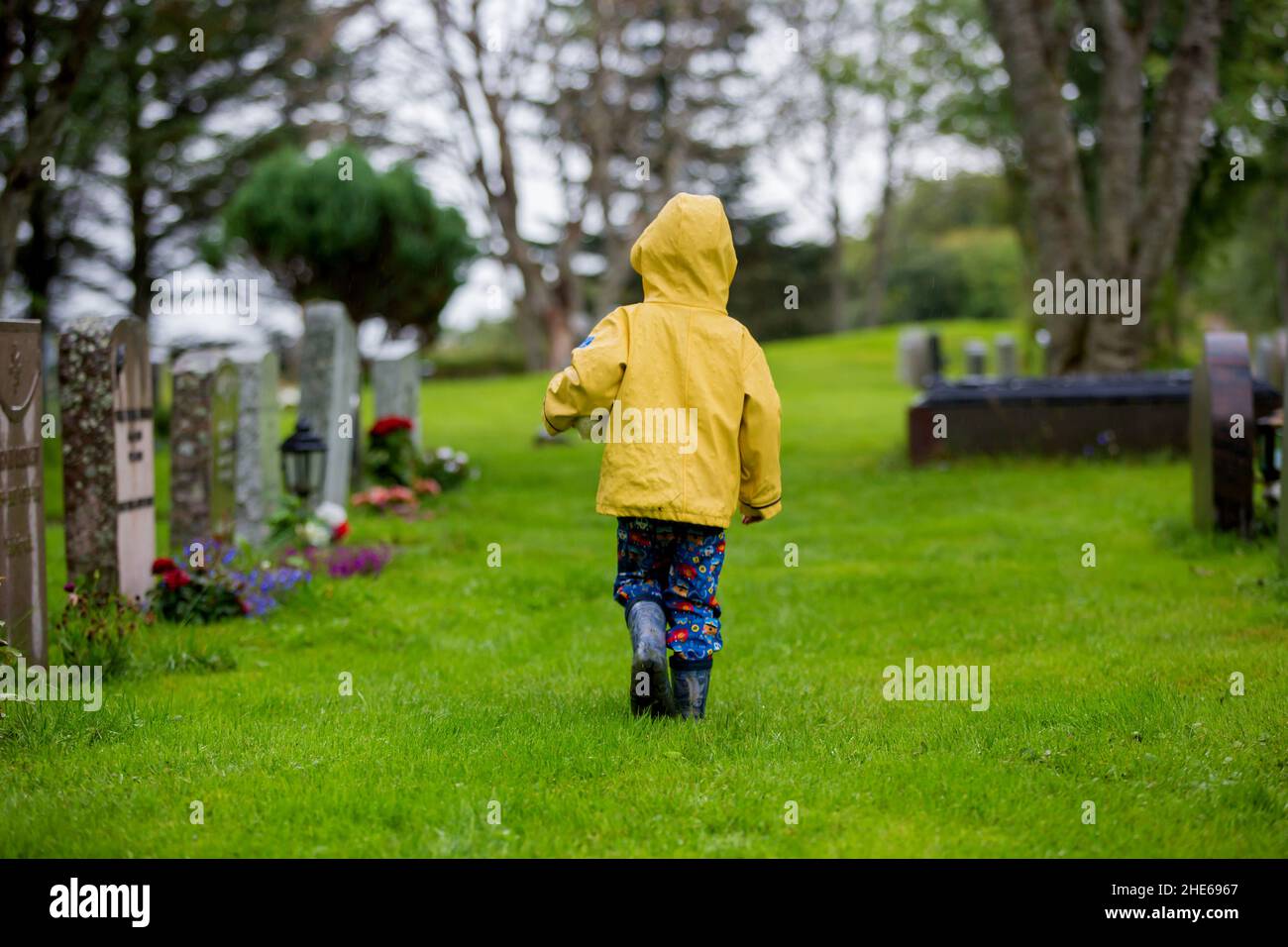 Sad little child, blond boy, standing in the rain on cemetery, sad ...