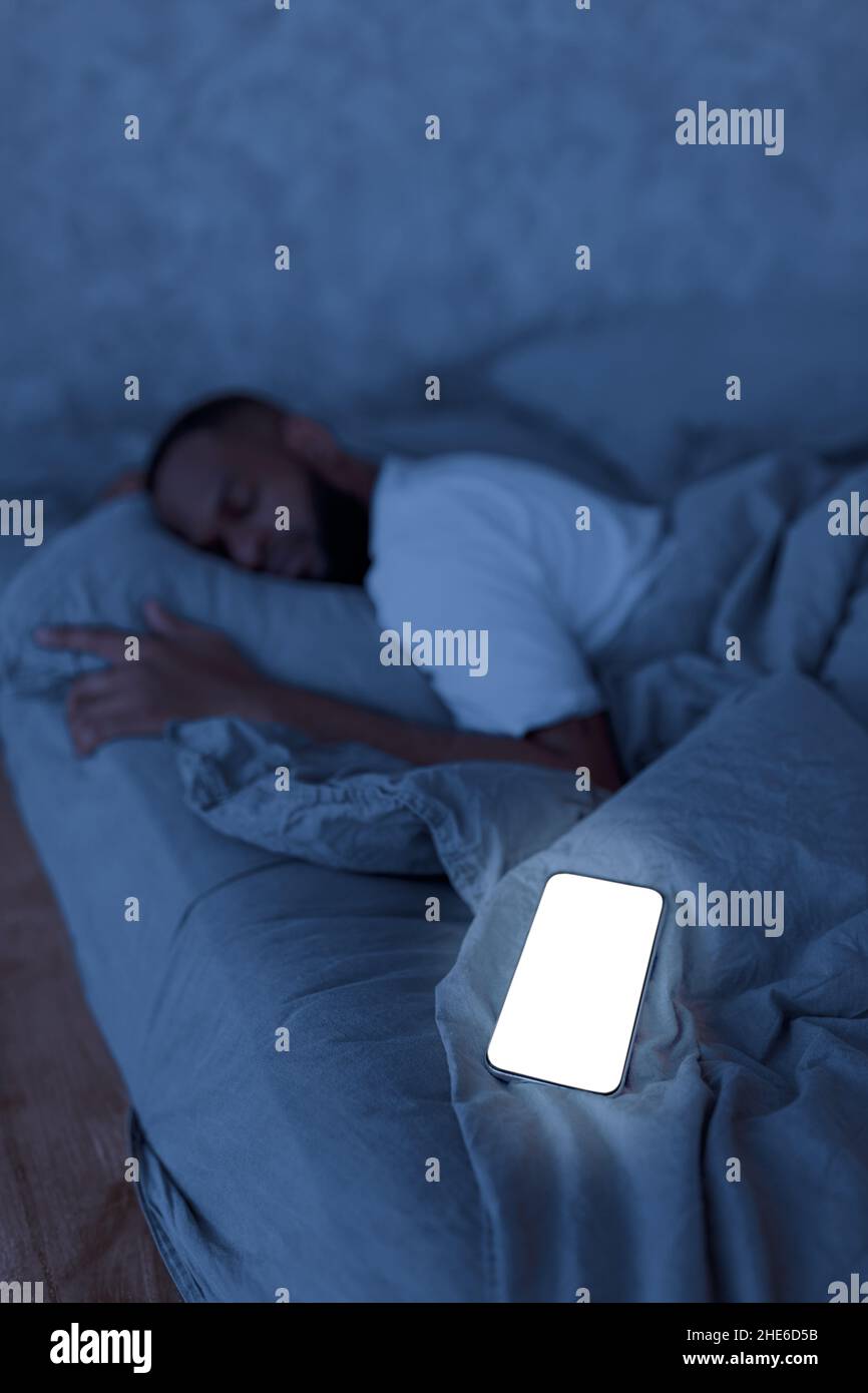 Young African American man sleeping in bed with cellphone Stock Photo ...