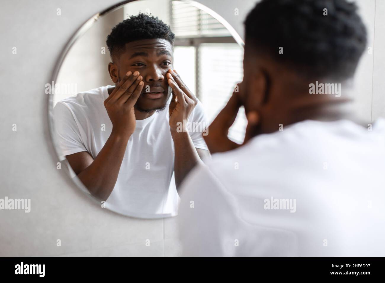 Sleepy black man touching black circles under eyes in bathroom Stock ...